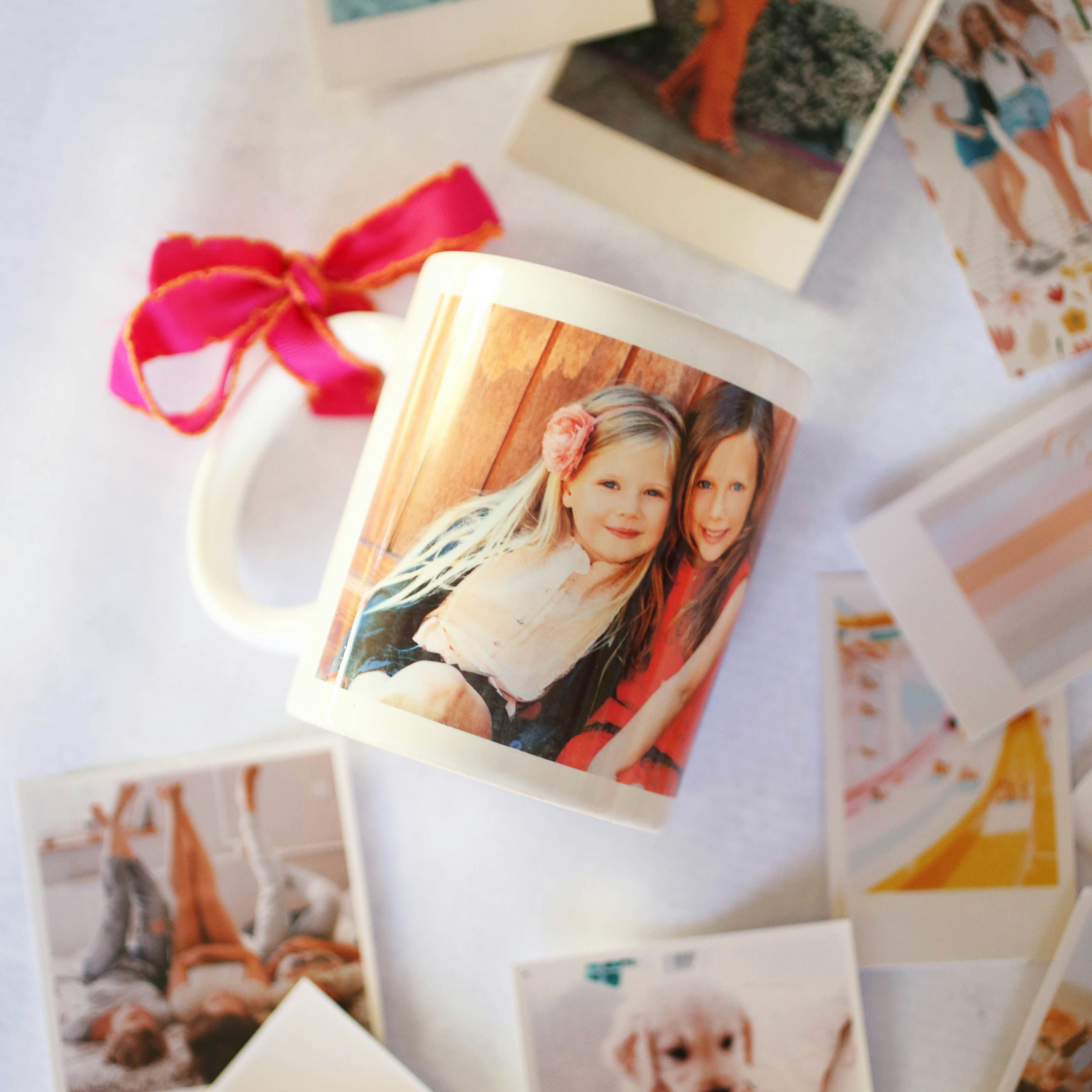 Personalized mug featuring a photo of two young girls, surrounded by various polaroid-style images on a soft surface.