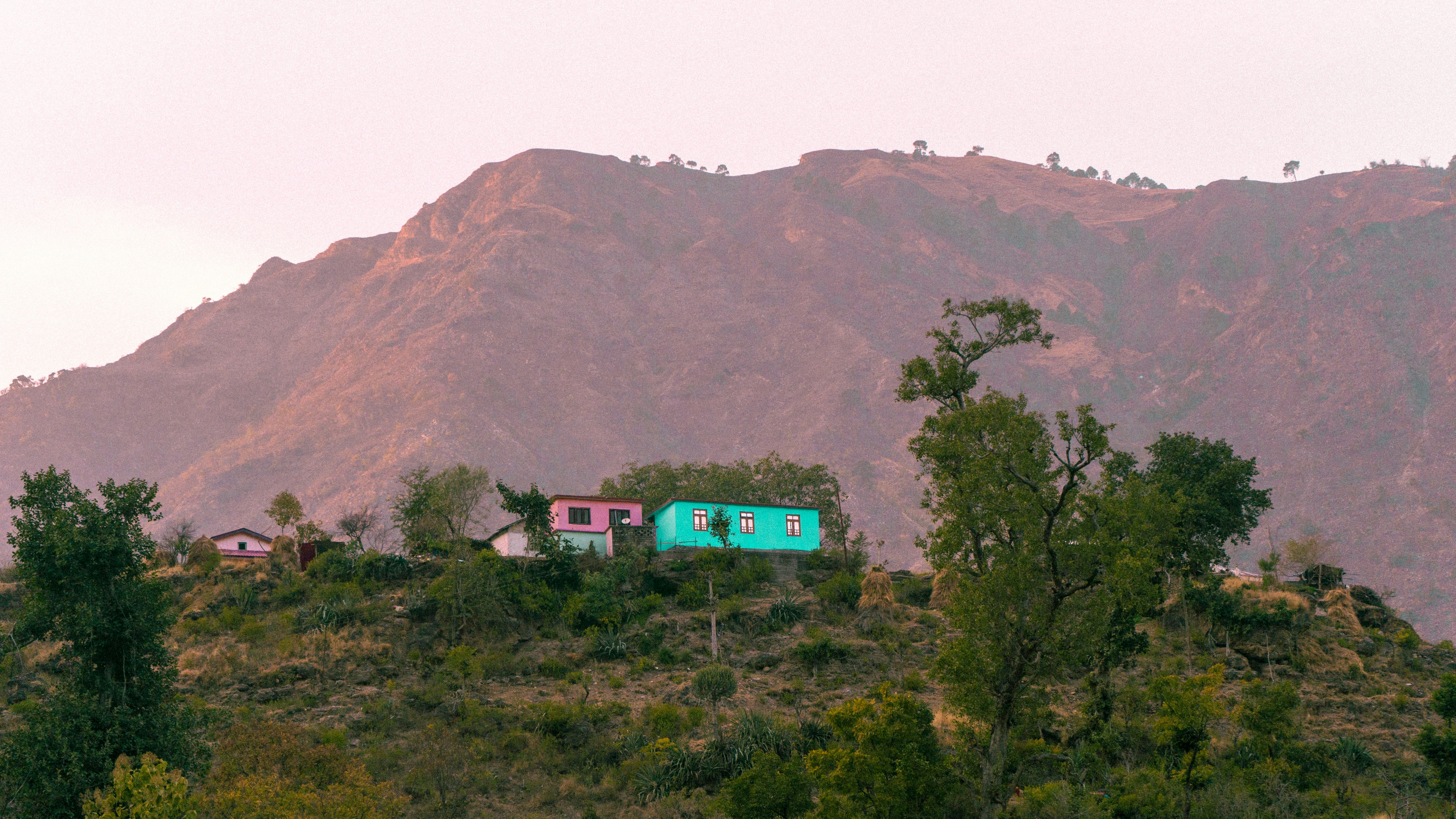 A colorful house nestled on a hillside, surrounded by lush greenery and towering mountains in the background.