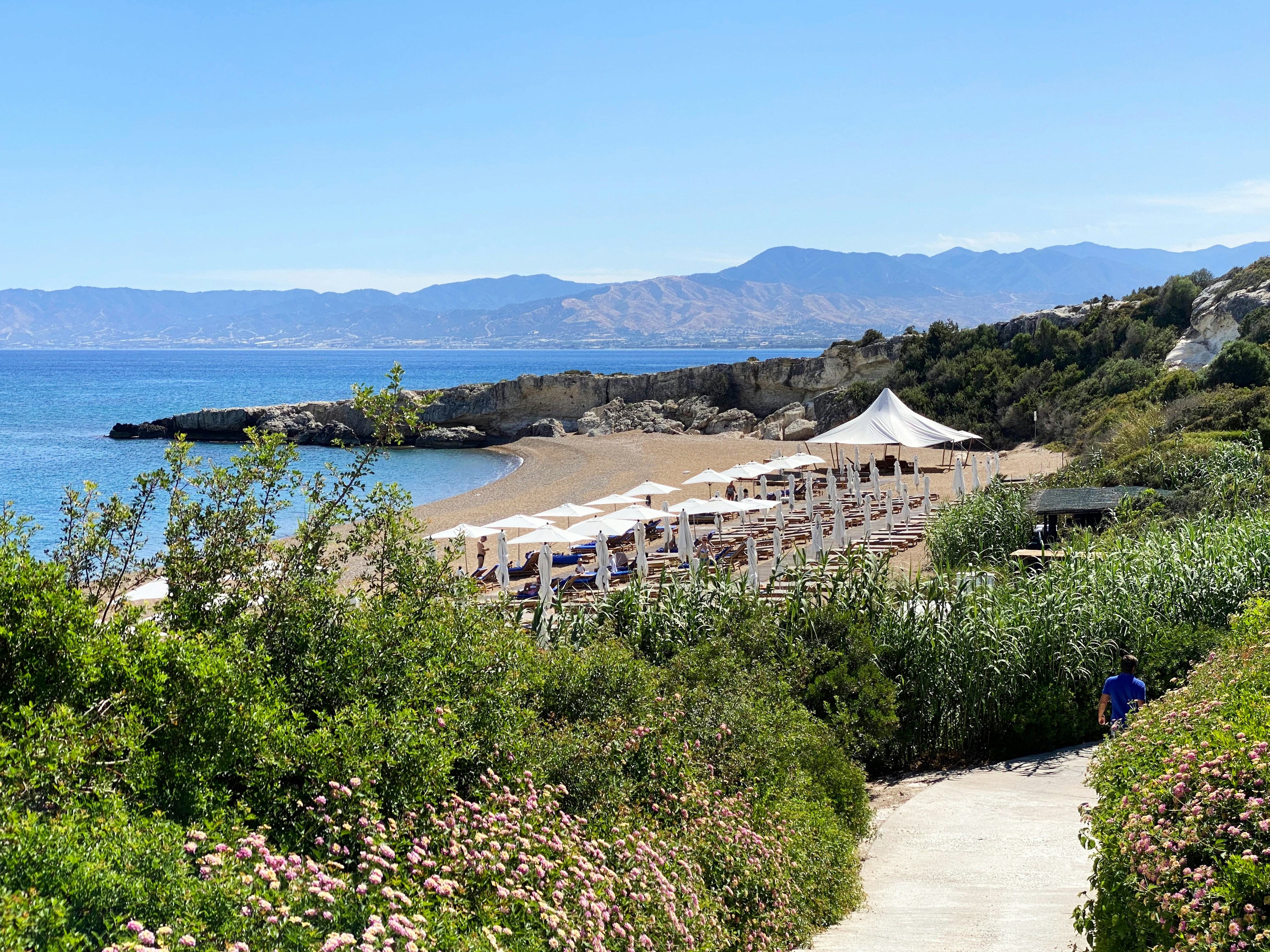 Idyllic beach scene with sun loungers and a tent, framed by lush greenery and mountains in the distance.