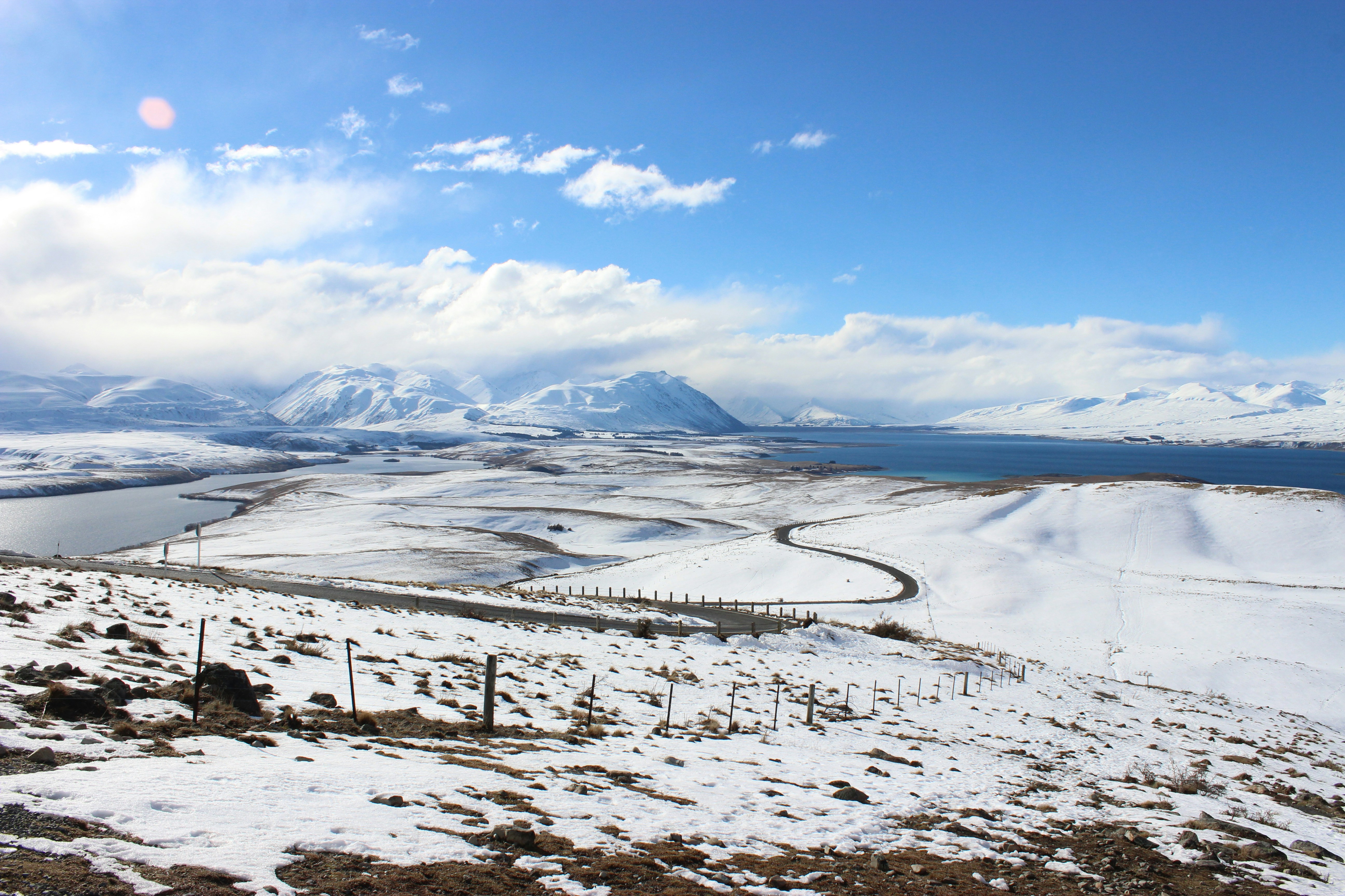 Snow-covered landscape with a winding road under a bright blue sky and scattered clouds.