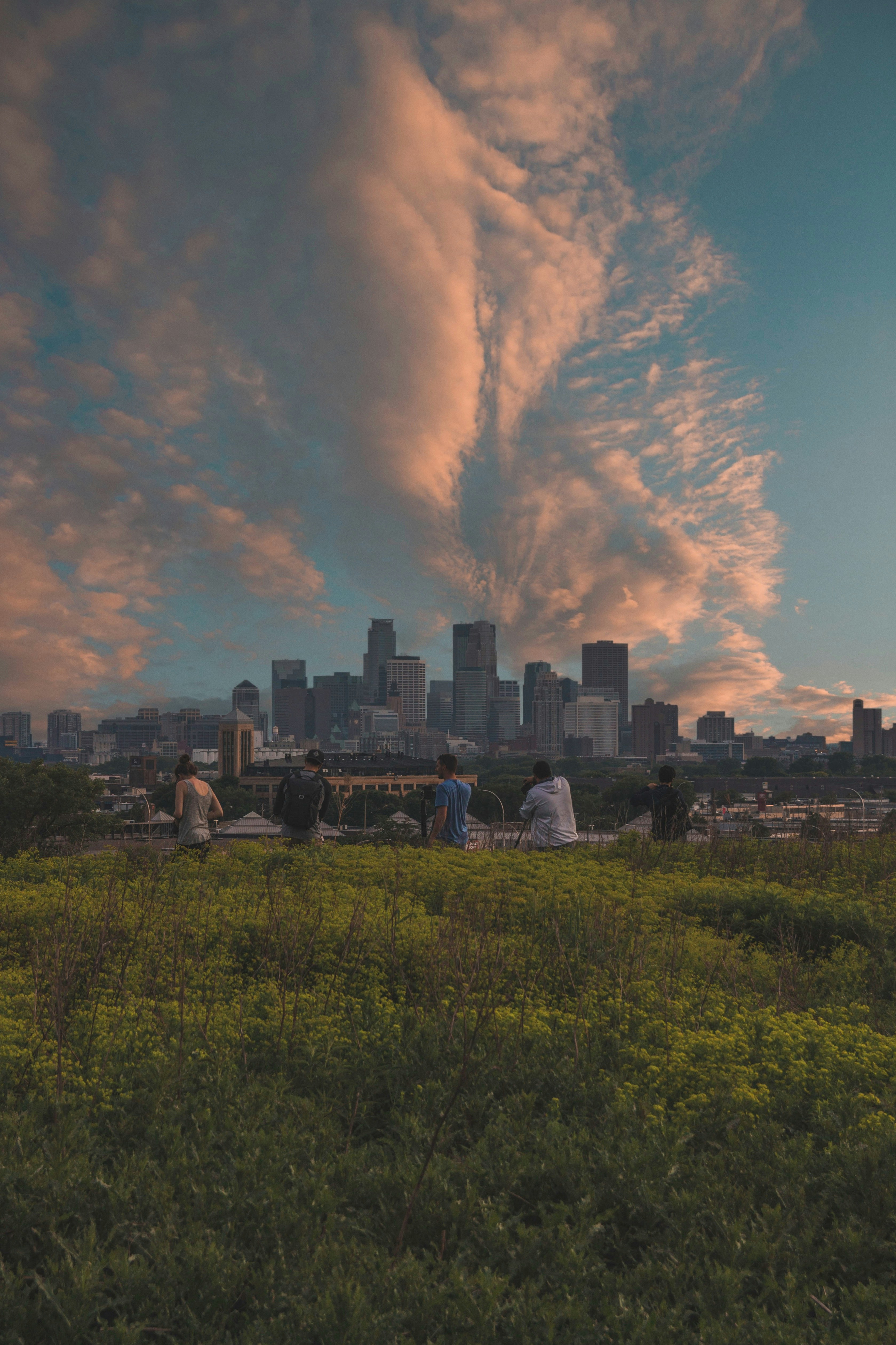Friends taking photographs of the Minneapolis skyline at sunset | people sitting on green grass field under blue sky during daytime