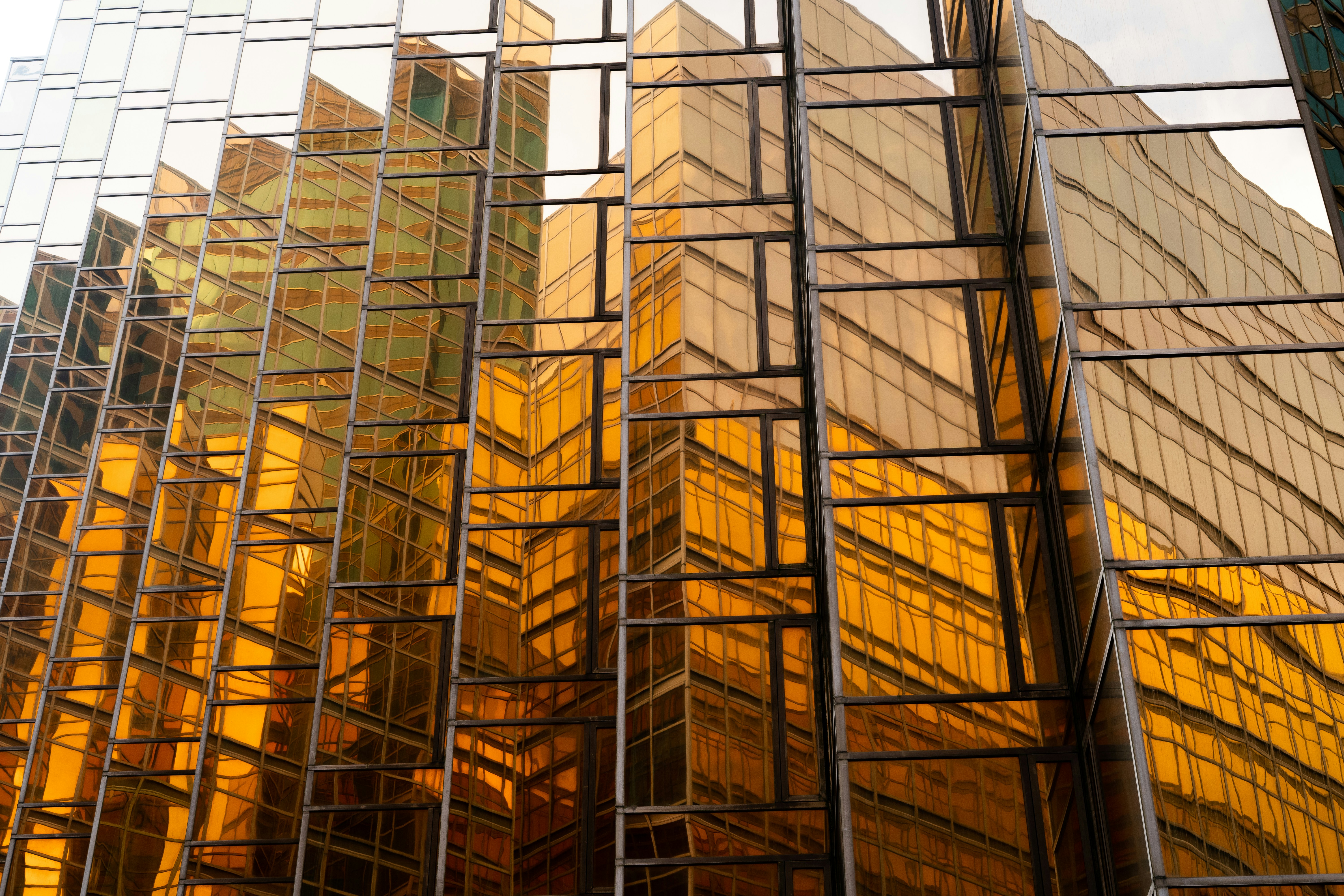 Reflective glass facade of a modern building showcasing intricate patterns and warm golden hues during sunset.