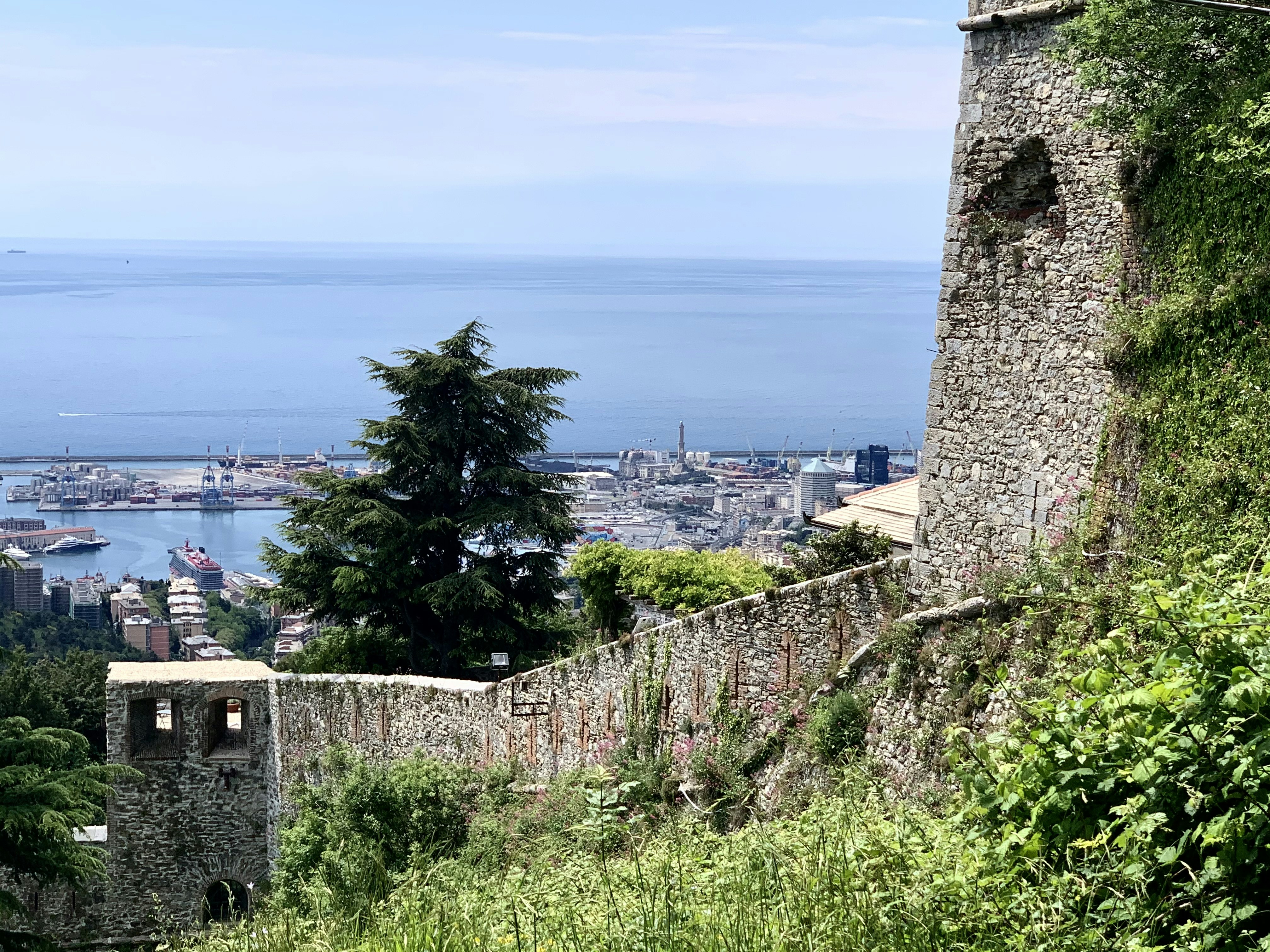 Stone fortress on a grassy hill with a seaside city in the distance.