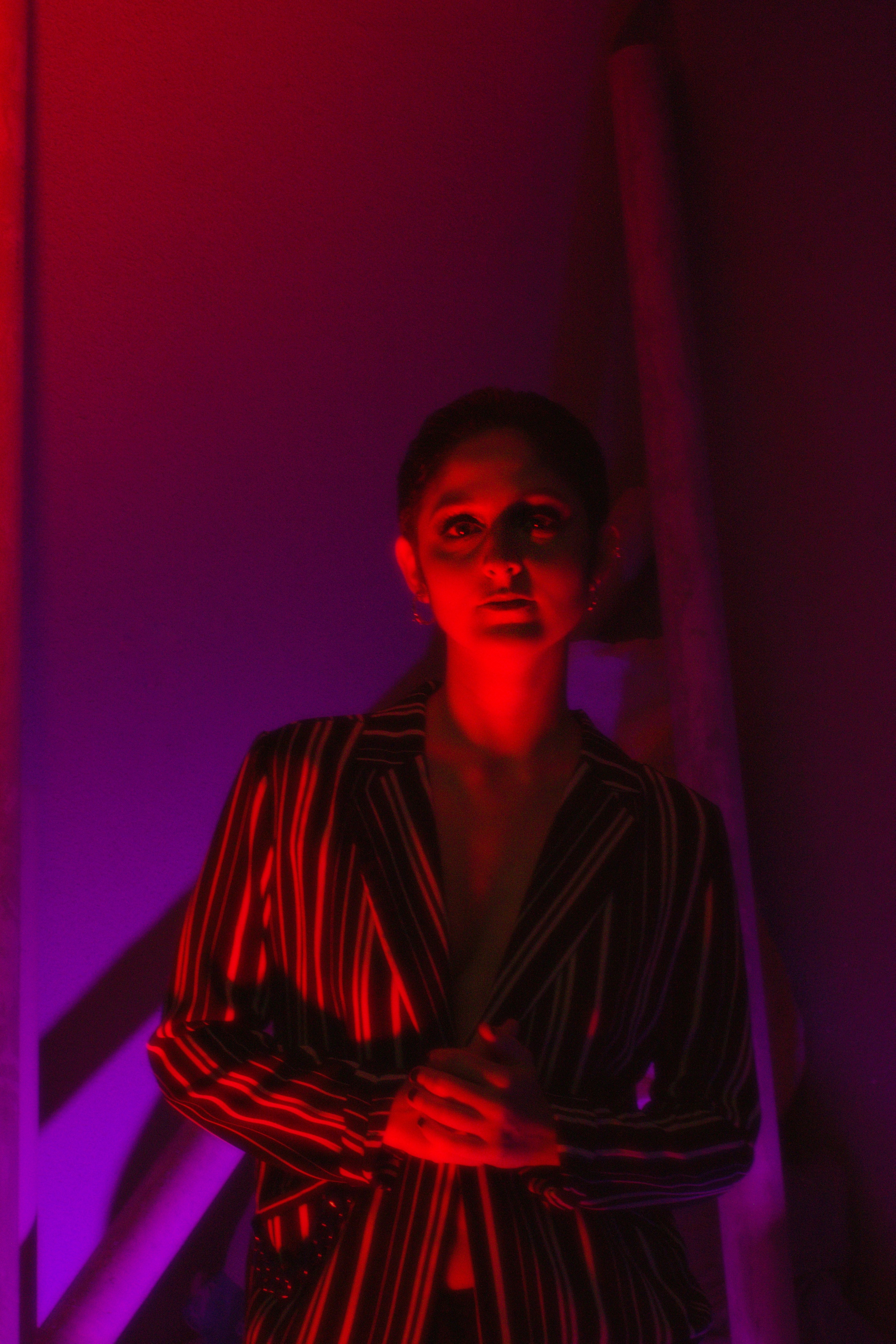 A figure in a striped blazer stands against a backdrop of vibrant red and purple hues, creating a moody and atmospheric scene.