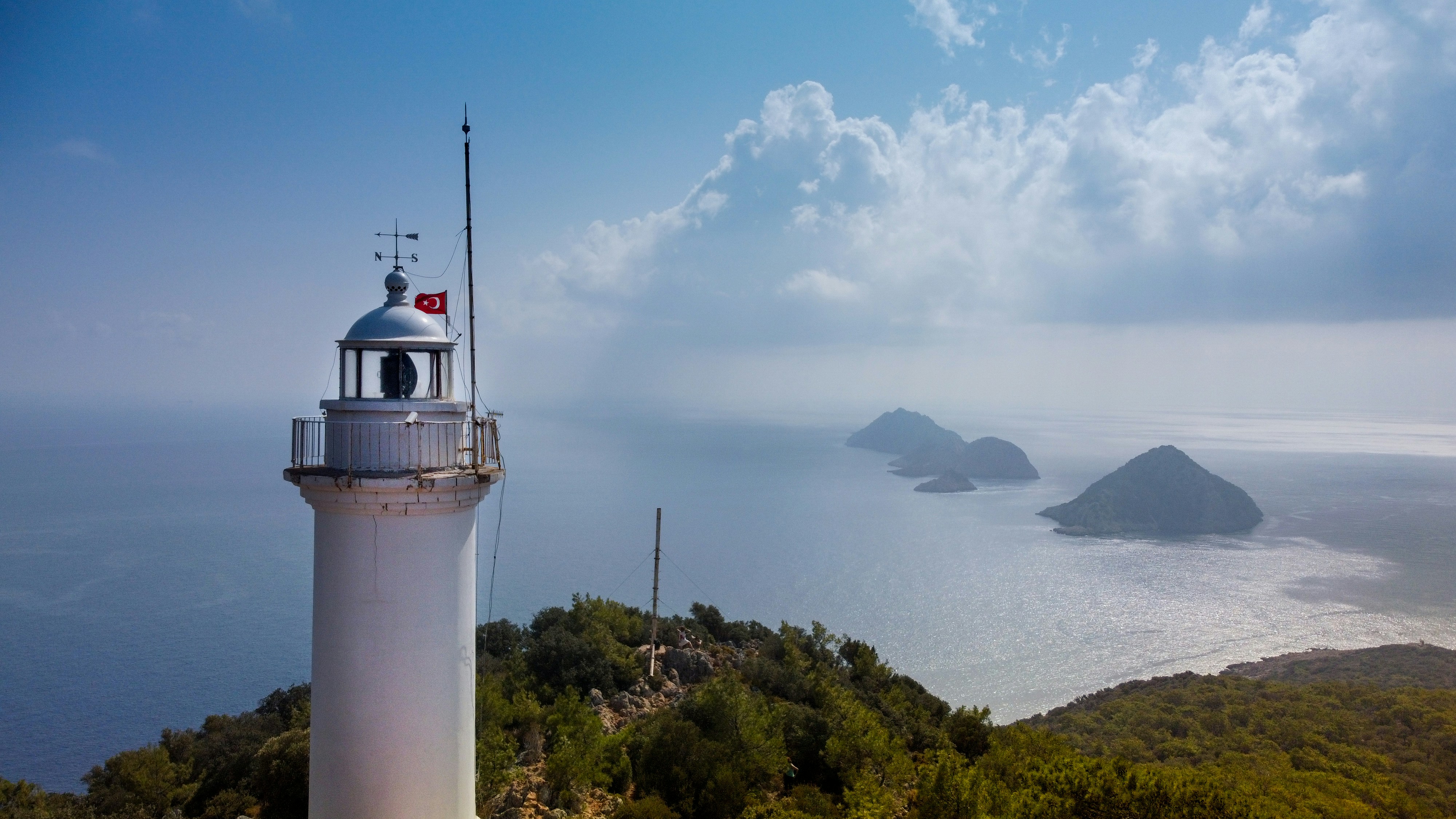 White lighthouse on a cliff with distant islands under a bright sky.