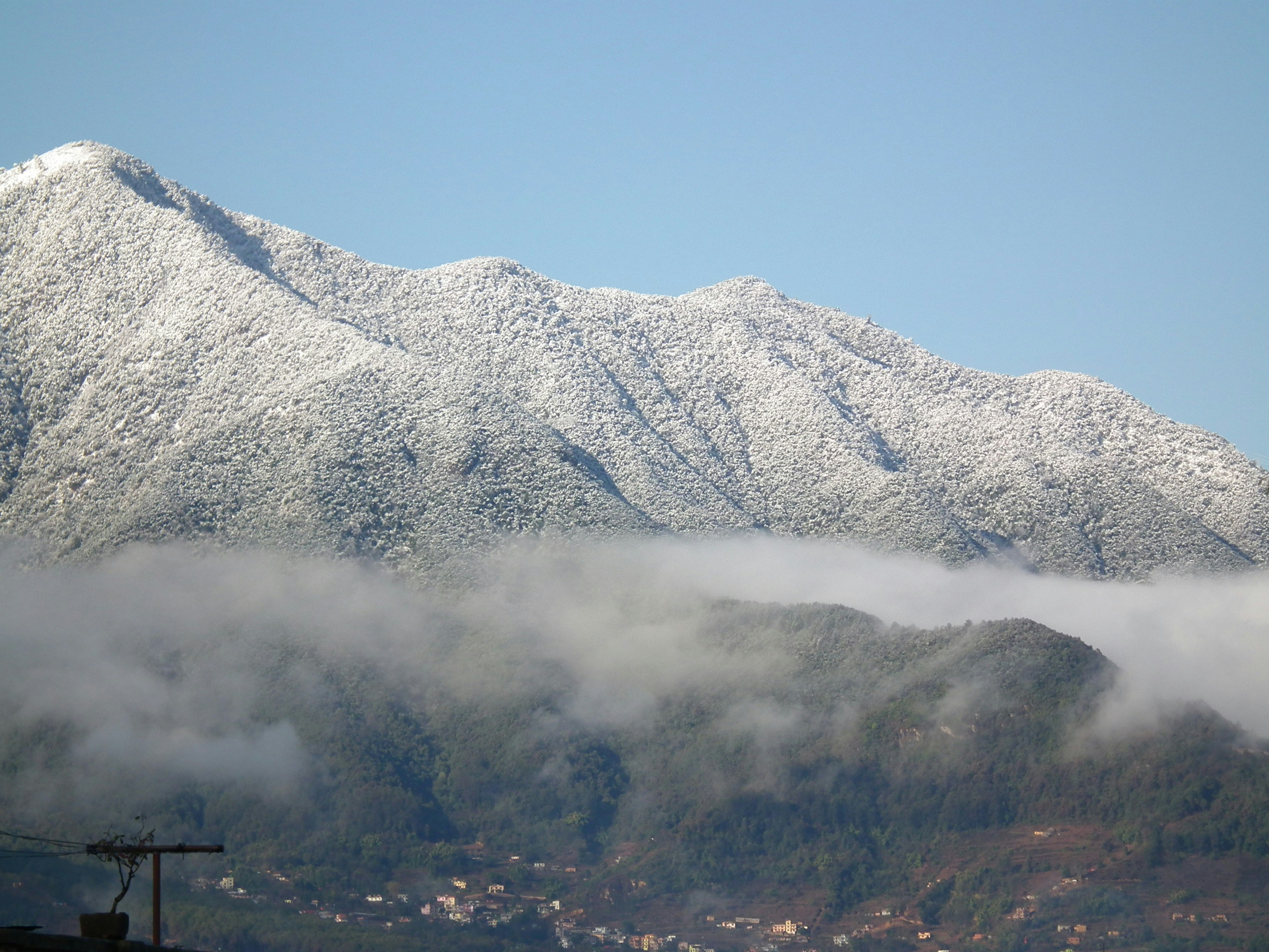 Majestic mountains draped in a blanket of snow rise above a sea of mist, revealing a tranquil landscape. The scene captures the serene beauty of winter's embrace.