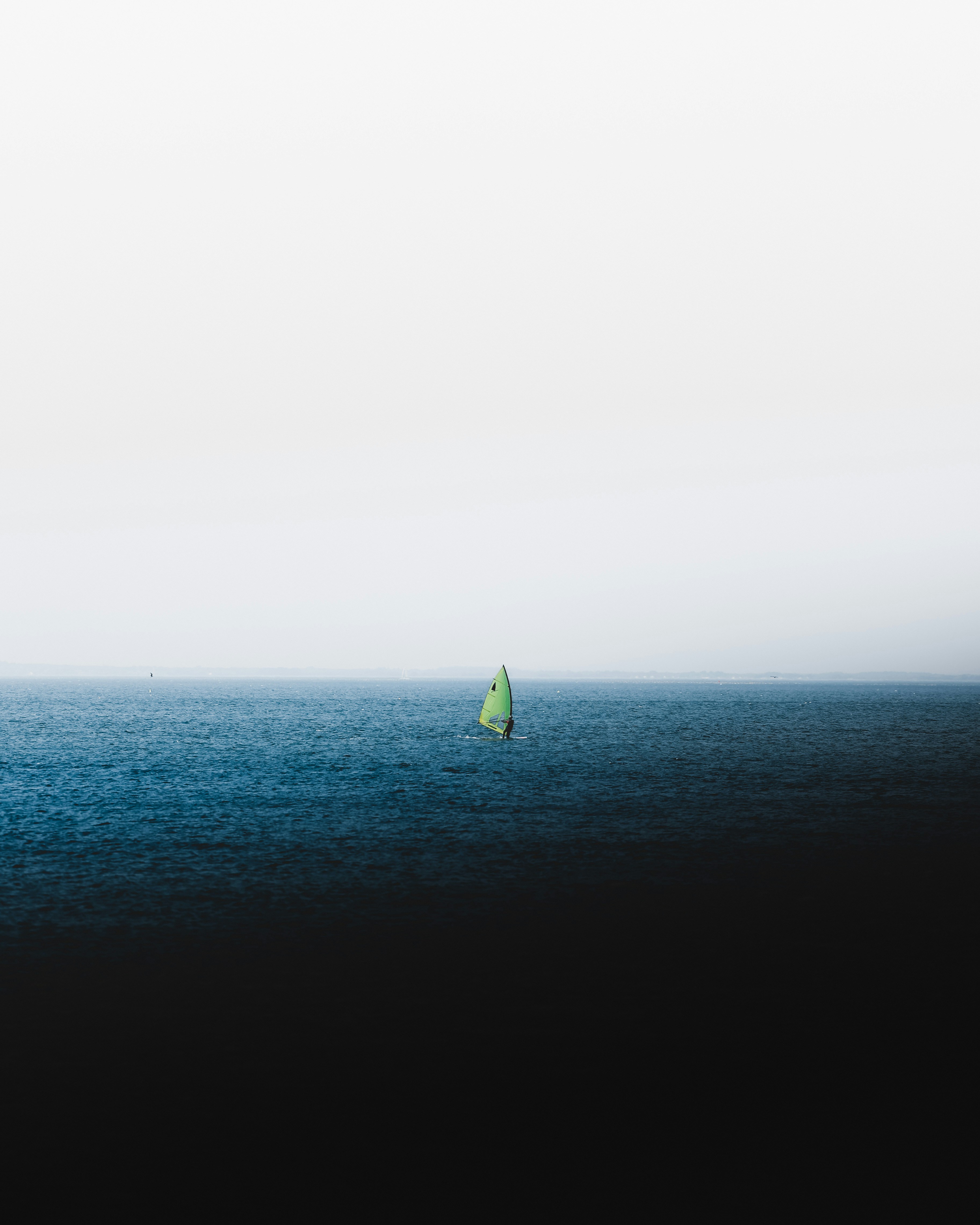 A lone sailboat with a vibrant green sail glides across a tranquil sea, surrounded by a soft gradient of light and shadow.