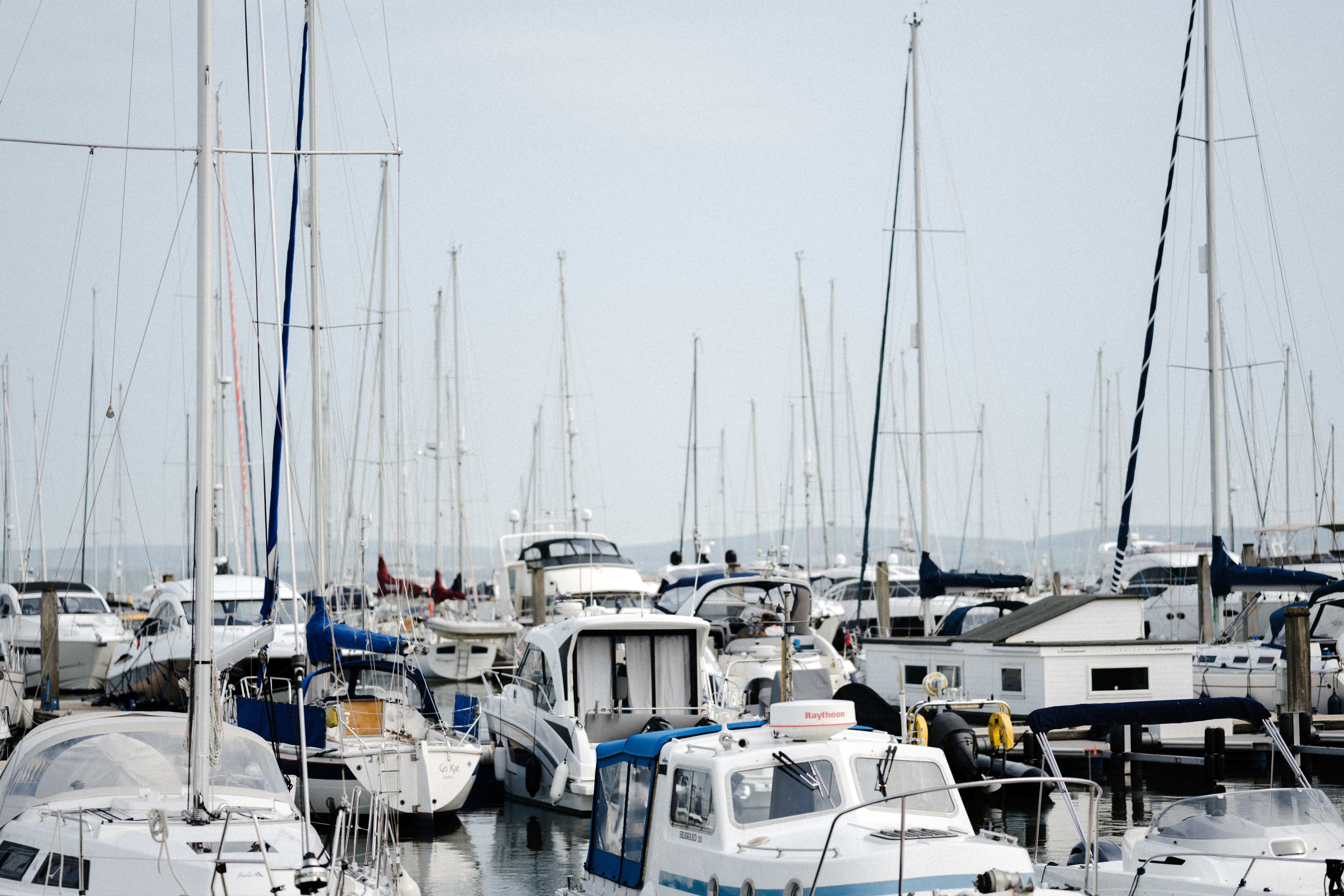 A bustling marina filled with various boats and yachts, showcasing the intricate arrangement of masts and hulls. The calm water reflects the scene's serene atmosphere.
