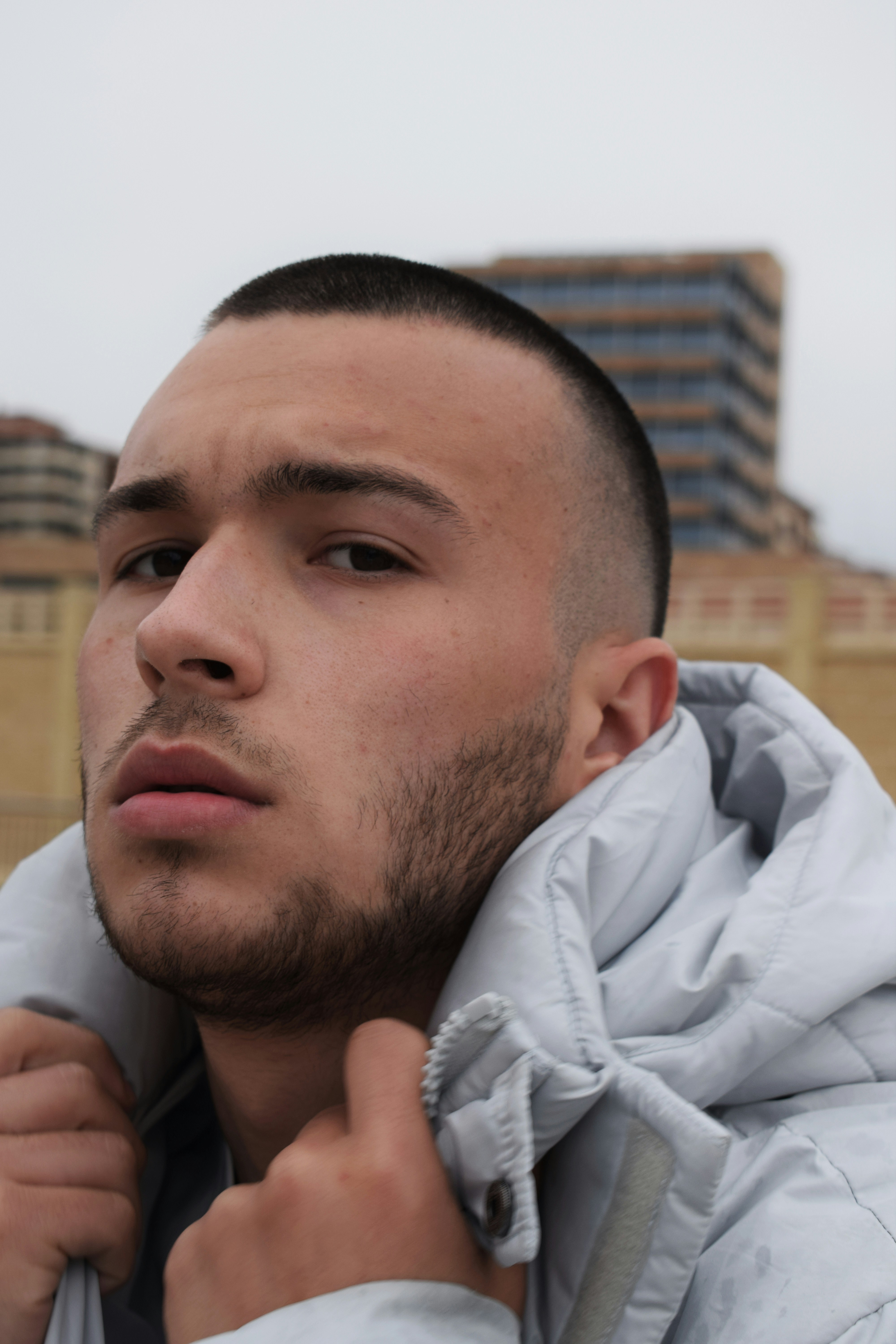Young man in a gray jacket gazing intently, set against a blurred urban backdrop.