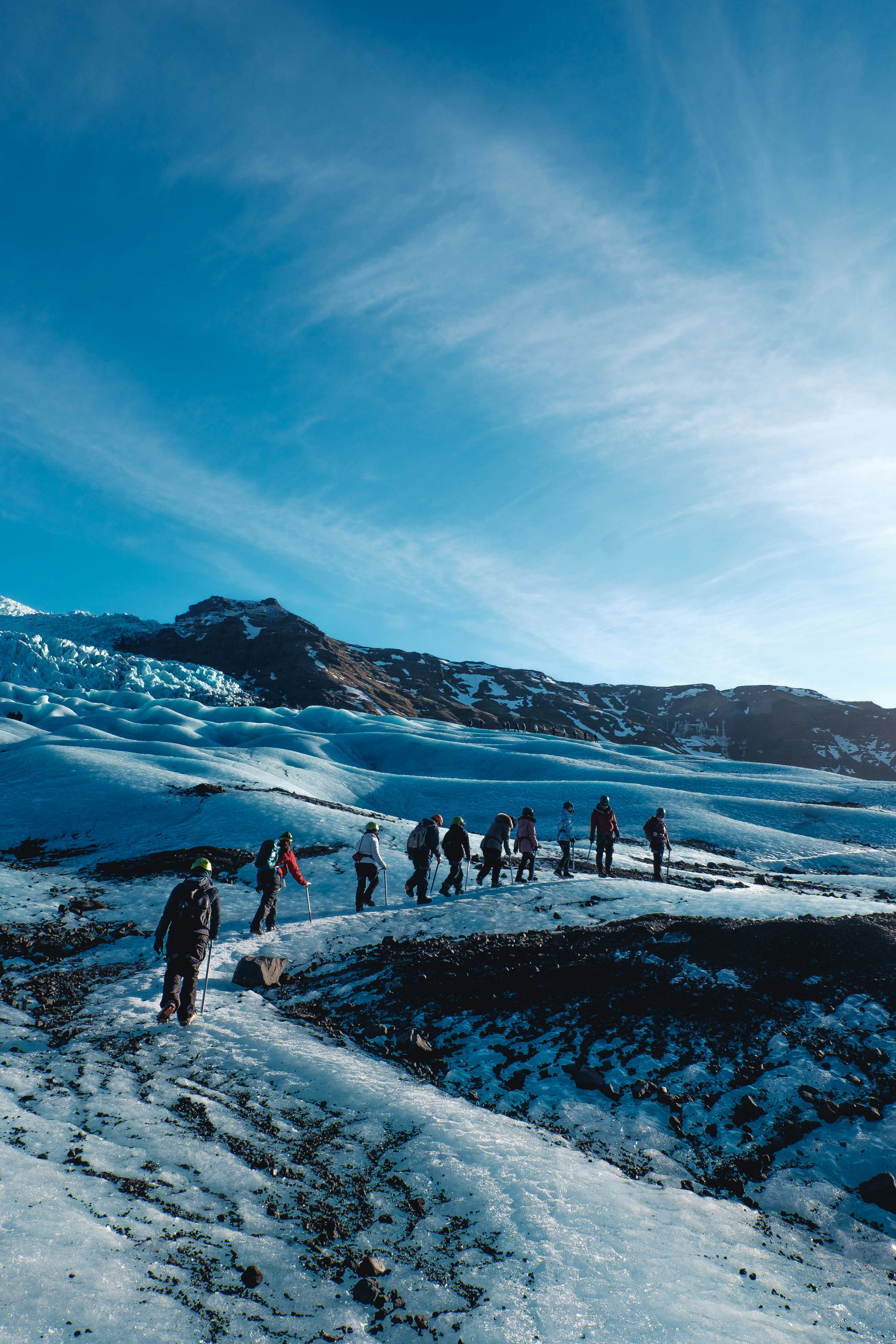 Group of adventurers traversing a blue glacier under a clear sky, showcasing the stark contrast between ice and volcanic terrain.