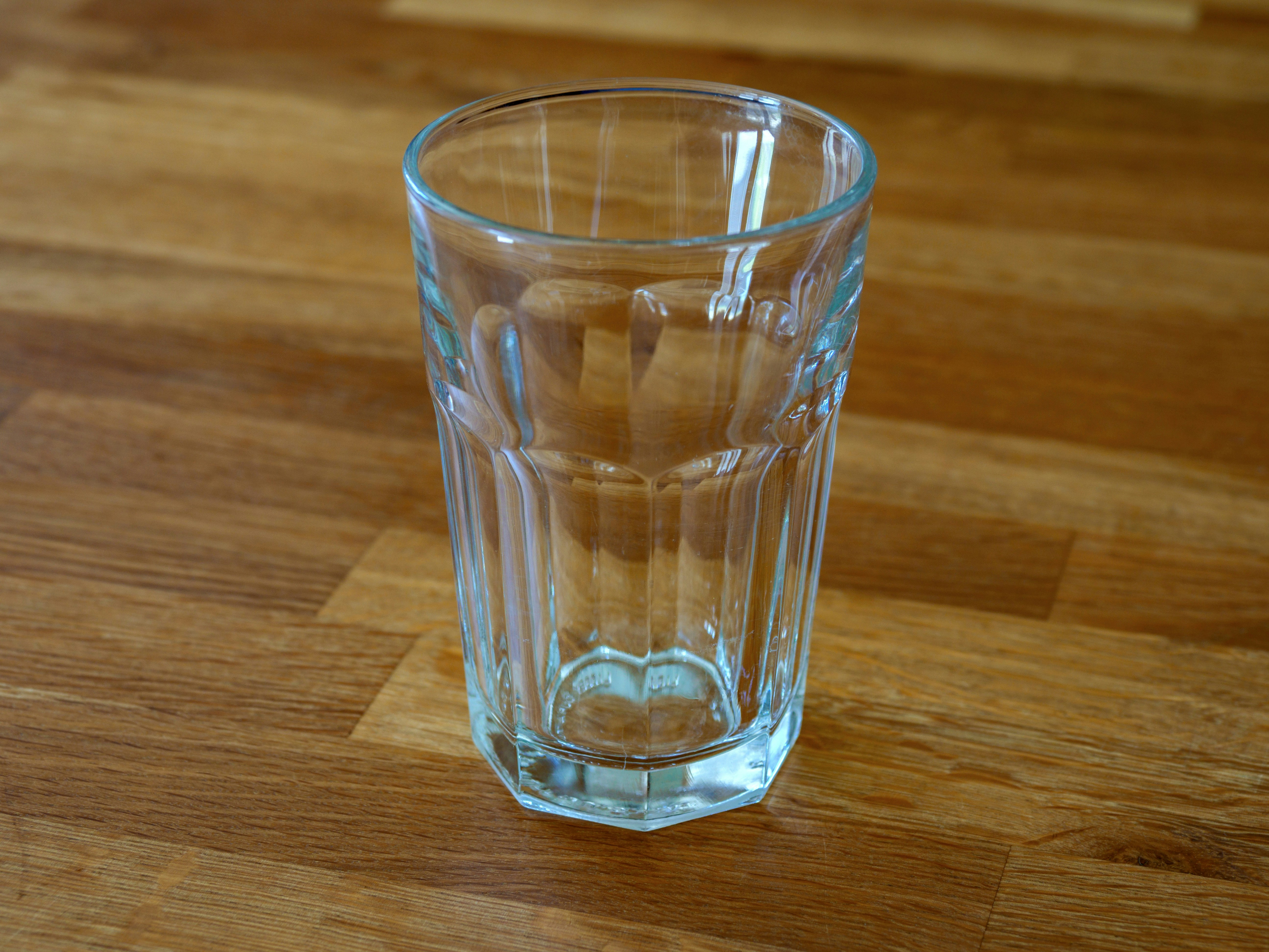 Clear glass tumbler resting on a wooden surface, showcasing its geometric design and reflections.