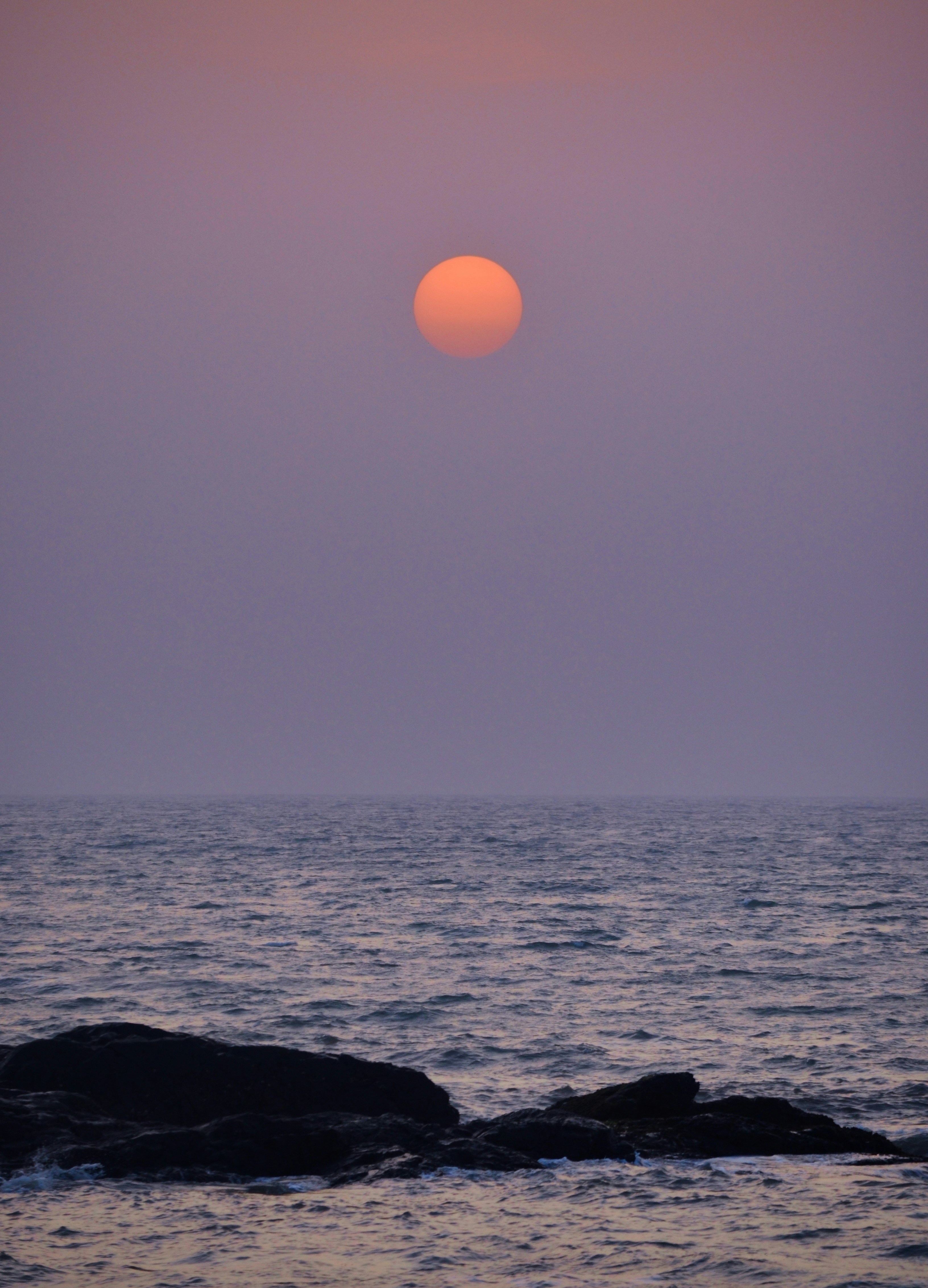 The sun is setting over the ocean with rocks in the foreground photo ...