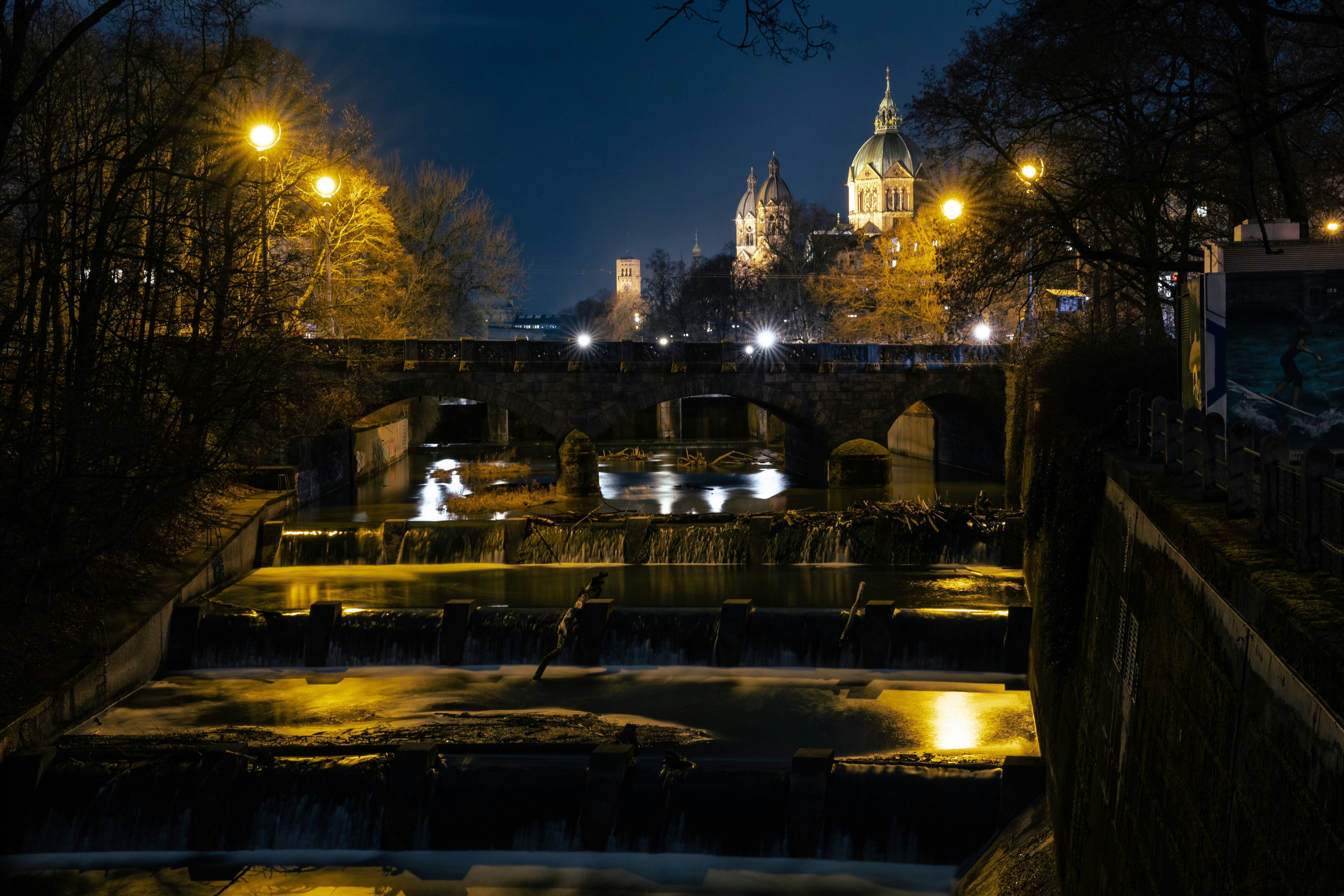 Illuminated cathedral and bridge with glowing streetlights and smooth waterfalls at night.