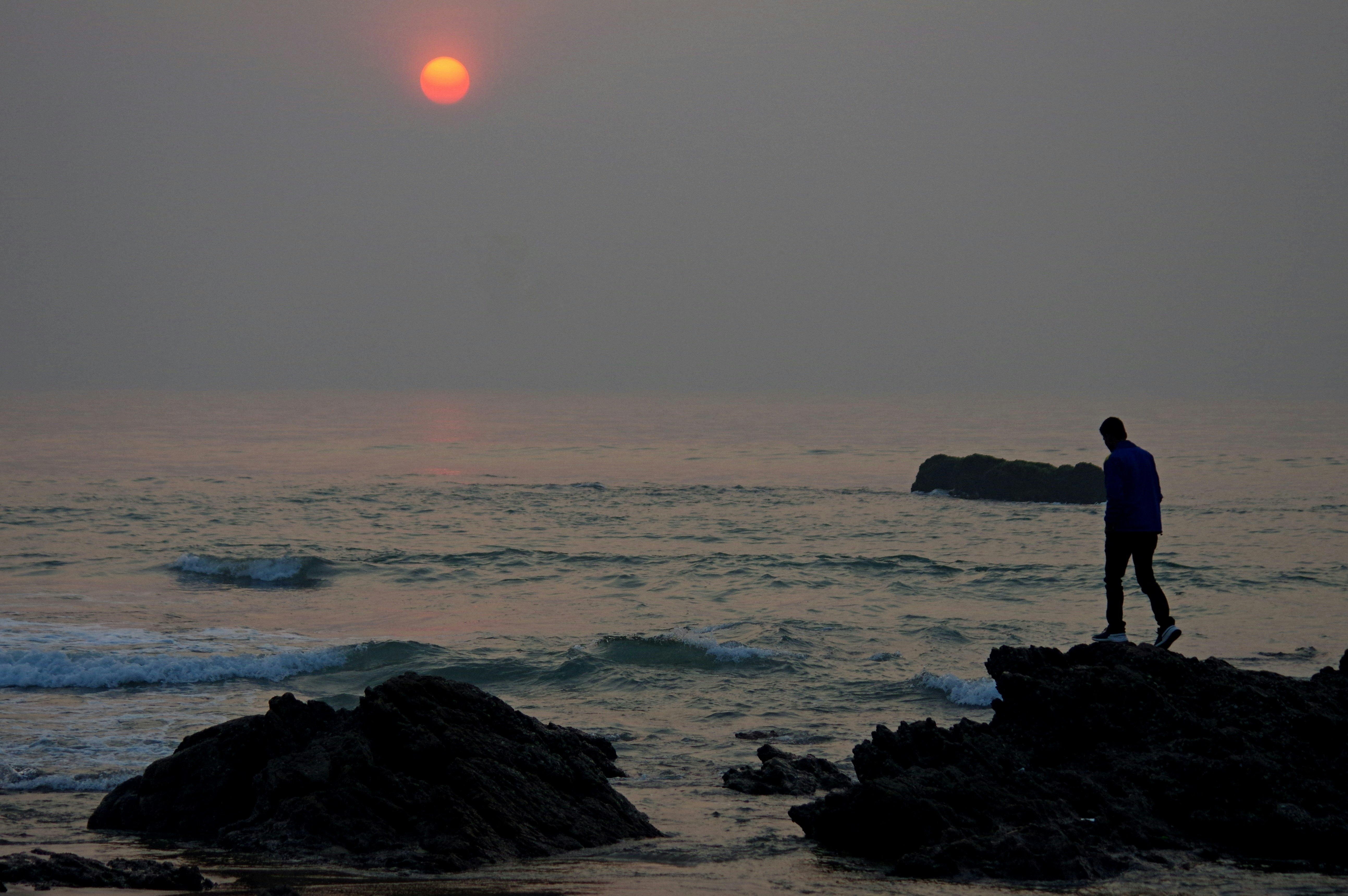 A man exploring sea rocks alongside Vishakapatnam's RK Beach at sunrise.