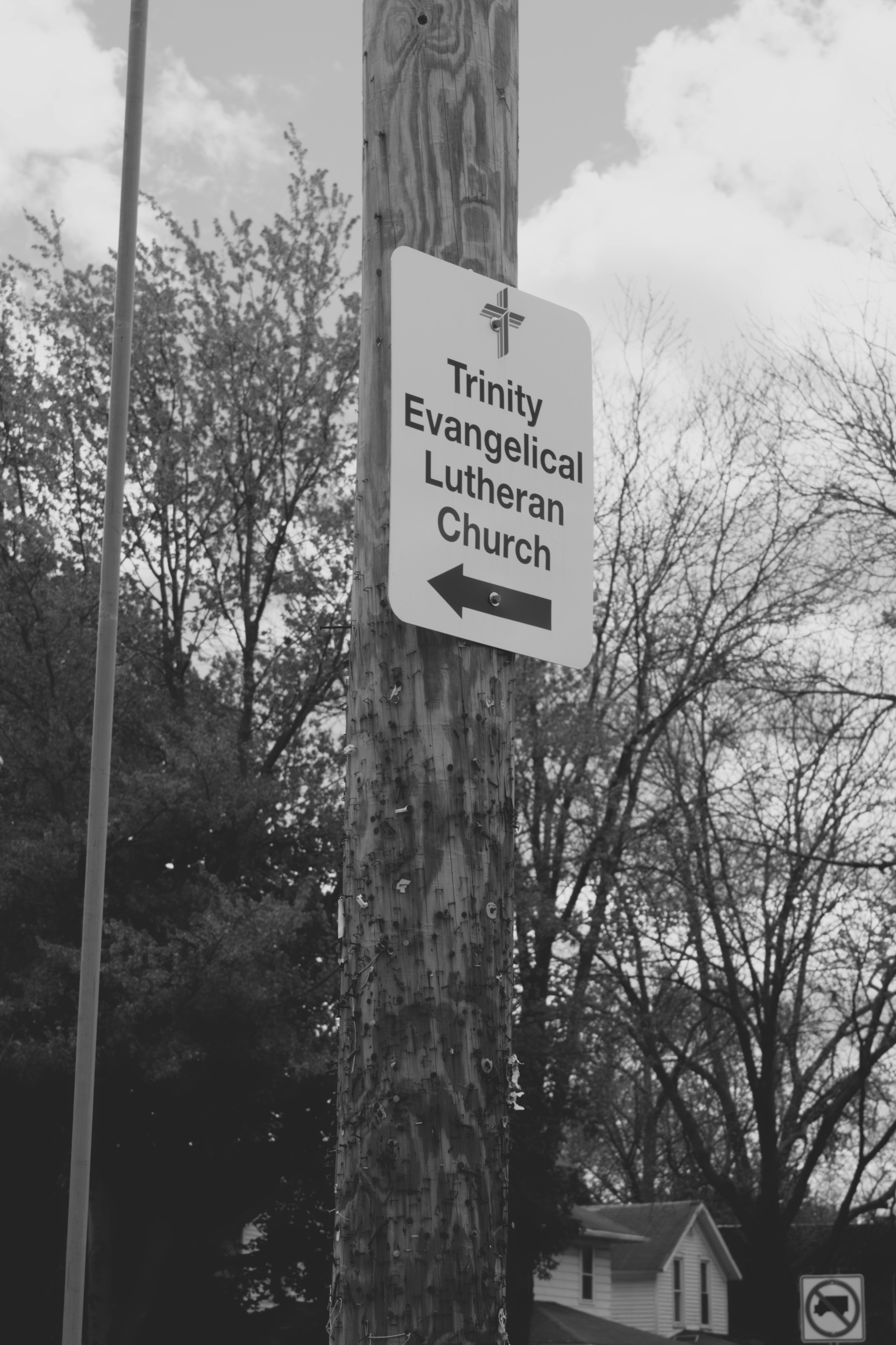 Sign directing to Trinity Evangelical Lutheran Church attached to a weathered utility pole amidst a backdrop of trees. 