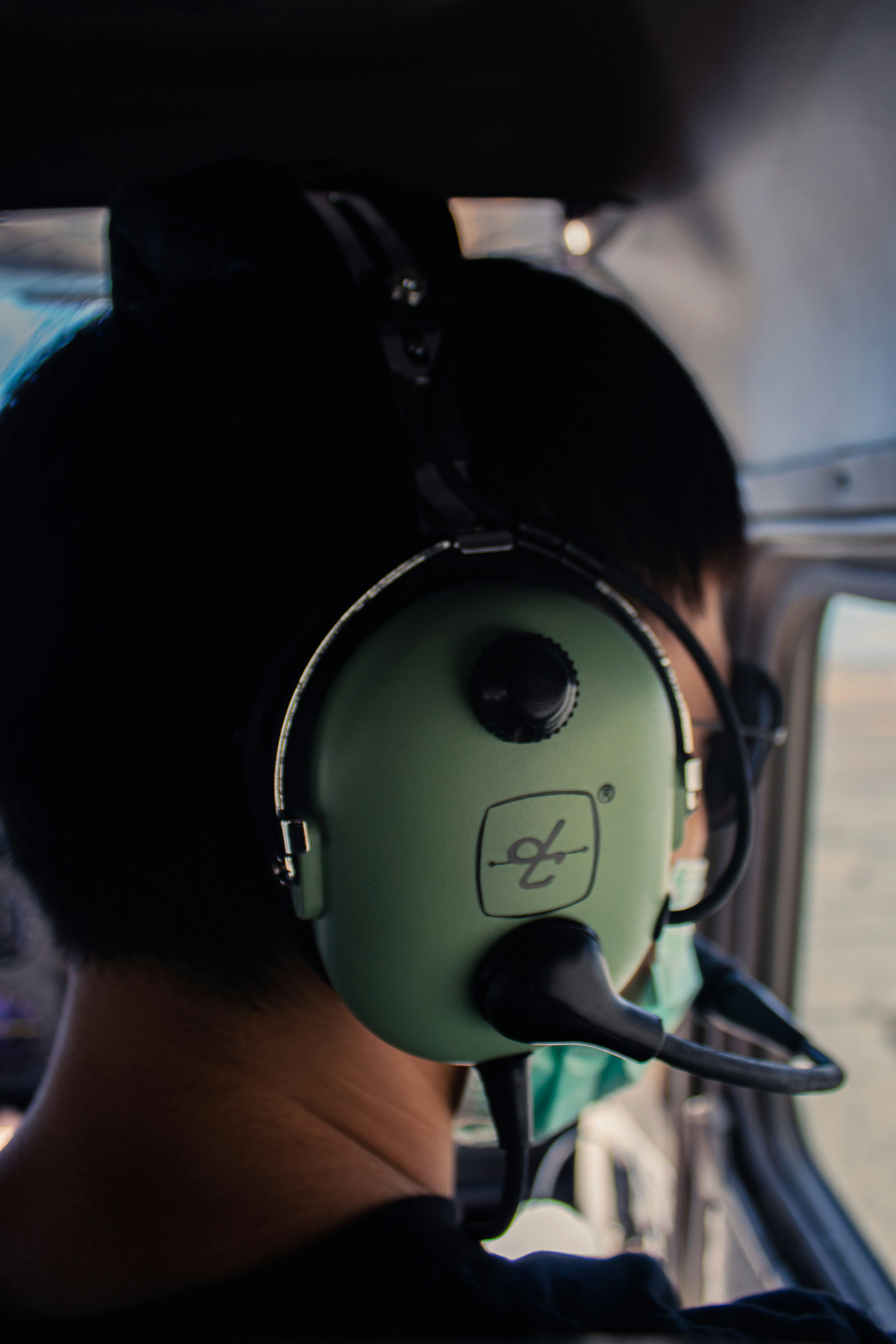 A close-up view of a pilot wearing green noise-canceling headphones, focused on the cockpit's controls. The scene captures the essence of aviation and concentration.
