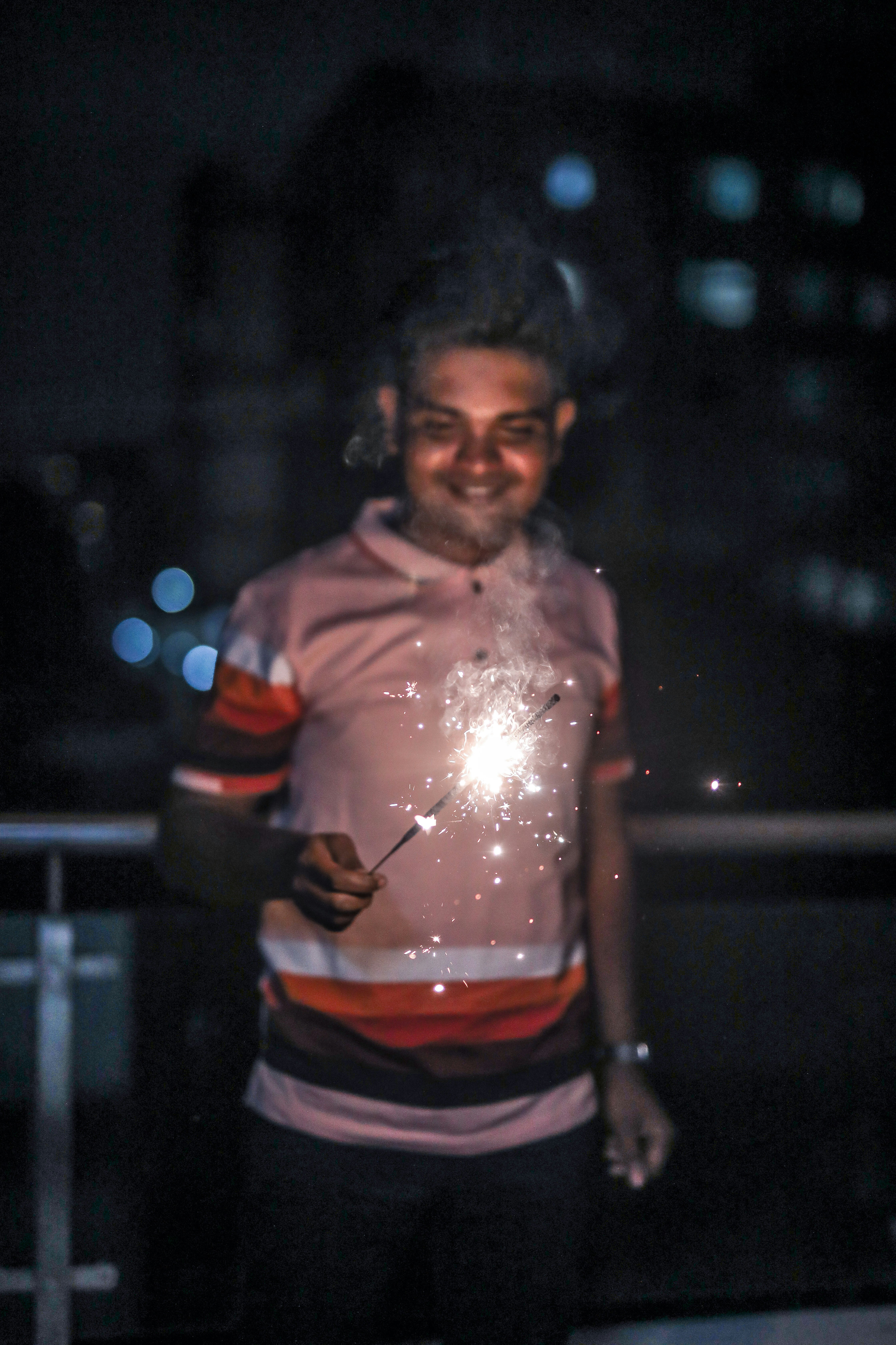 Person holding a sparkler, surrounded by a blurred urban night backdrop with glowing lights.
