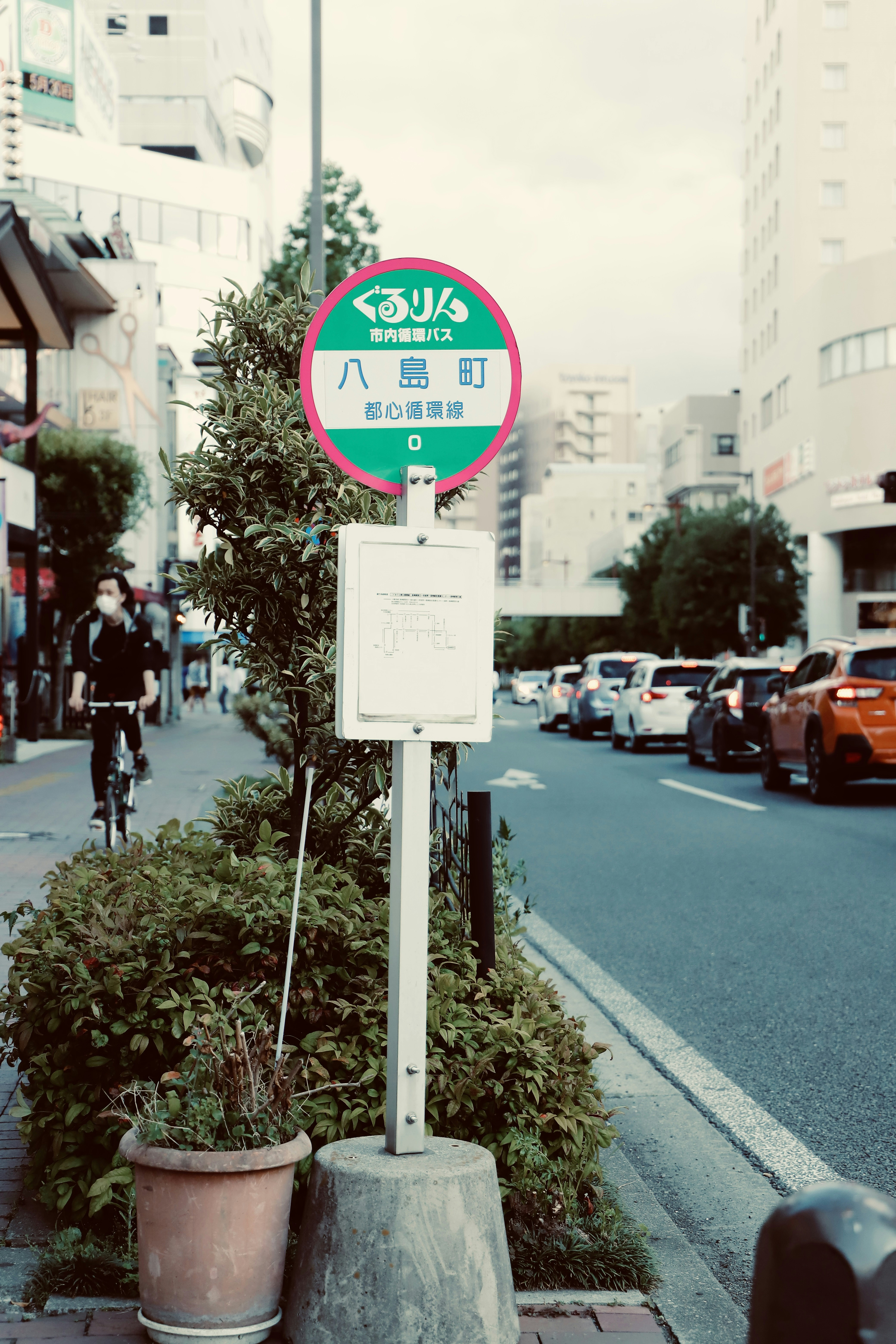 Circle of Transit: A Teal-Pink Bus Stop Sign Anchors a Lively Japanese Street