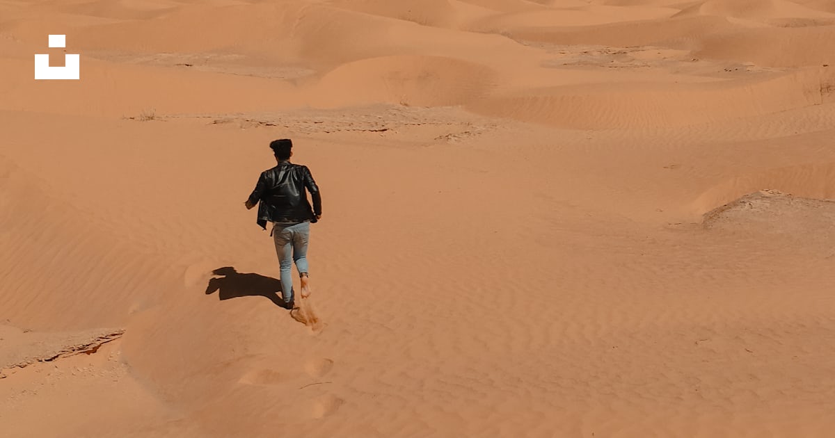 Hombre Con Chaqueta Negra Caminando Por El Desierto Durante El Día Foto