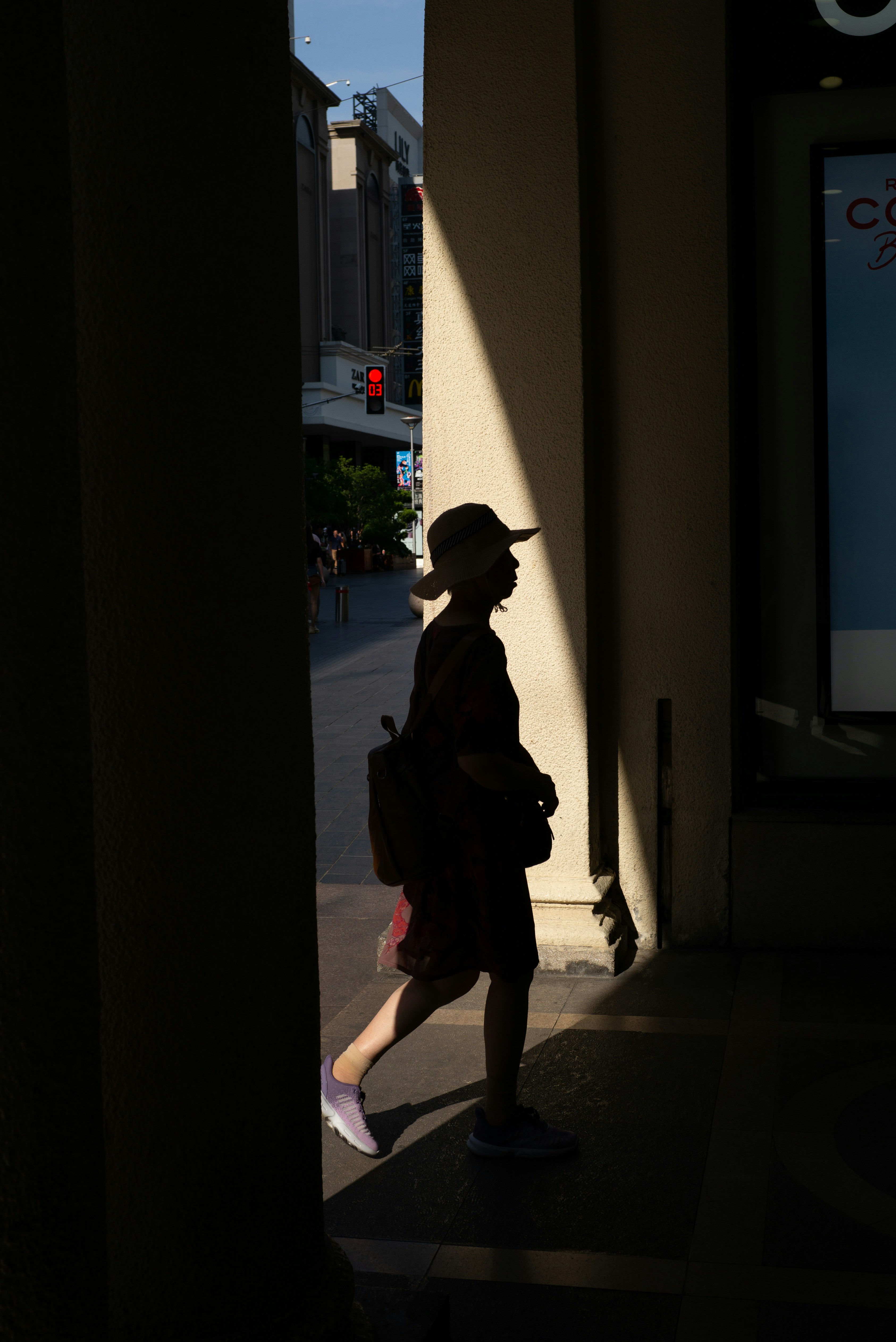 Silhouette of a woman walking through a sunlit archway, casting a long shadow against the wall. The scene captures the essence of urban exploration.