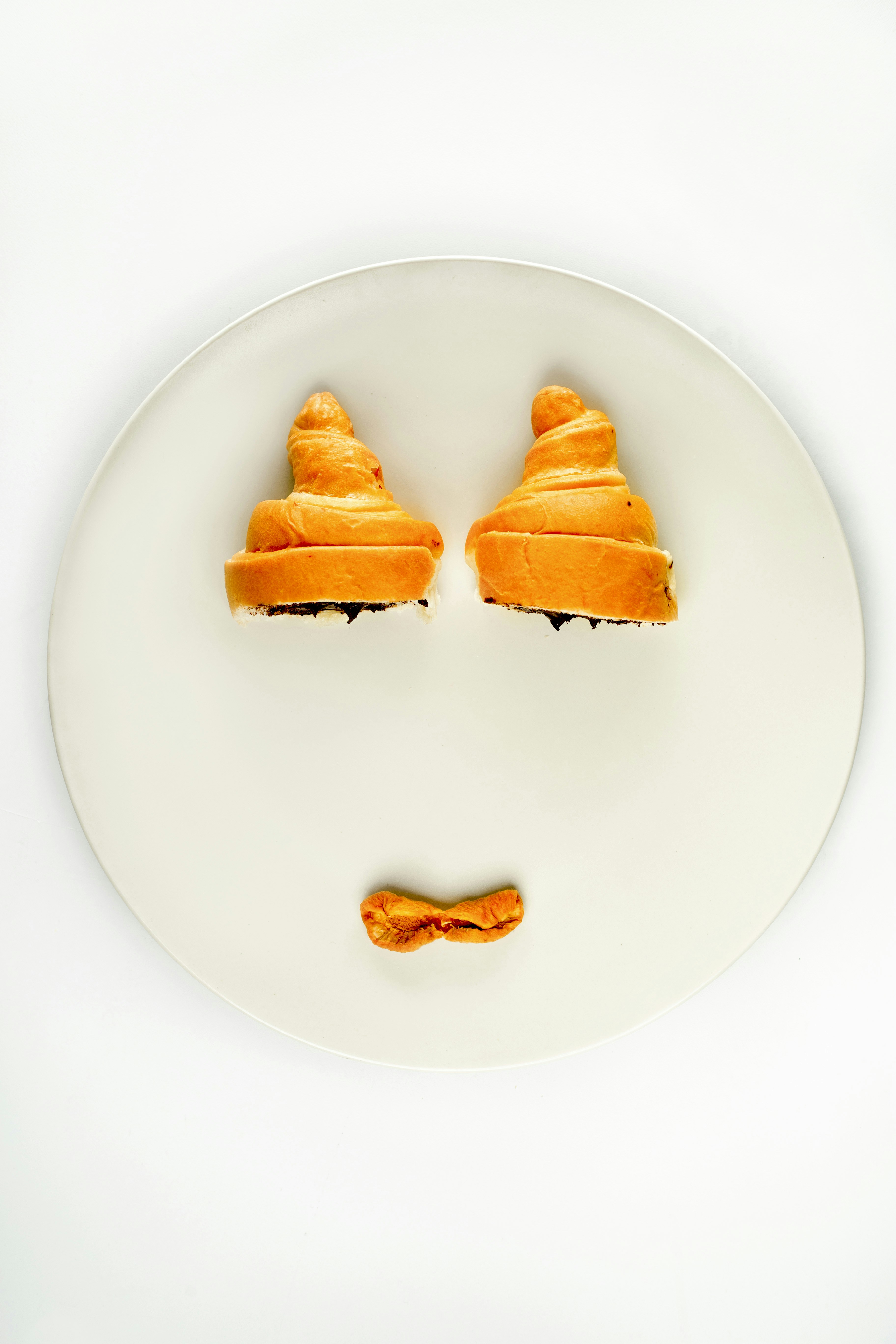 Whimsical Breakfast Face: Croissant Eyes and a Petite Smile on White Plate