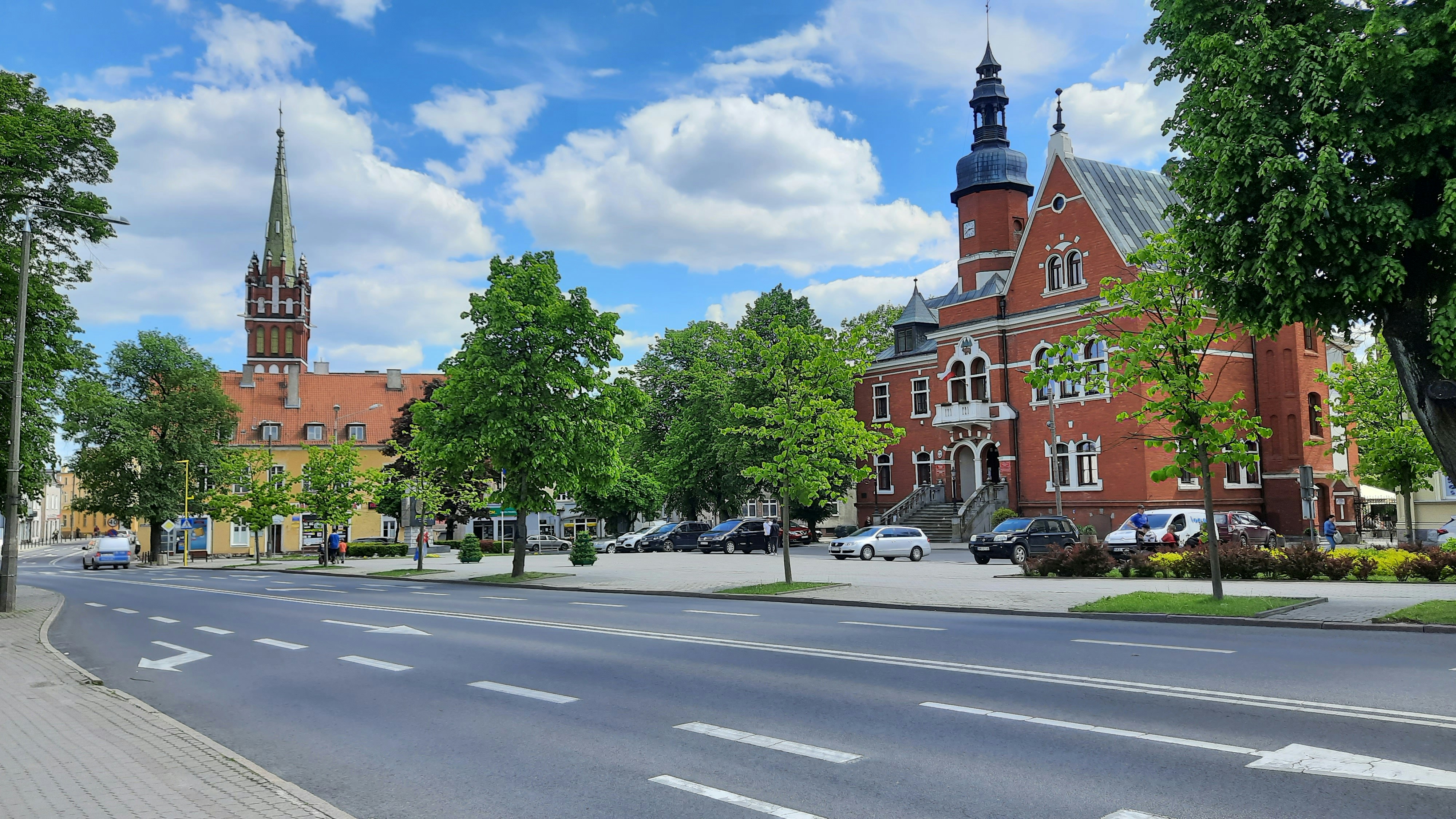 Historic red-brick buildings framed by lush greenery and a clear blue sky. The scene captures the essence of urban architecture blending with nature.