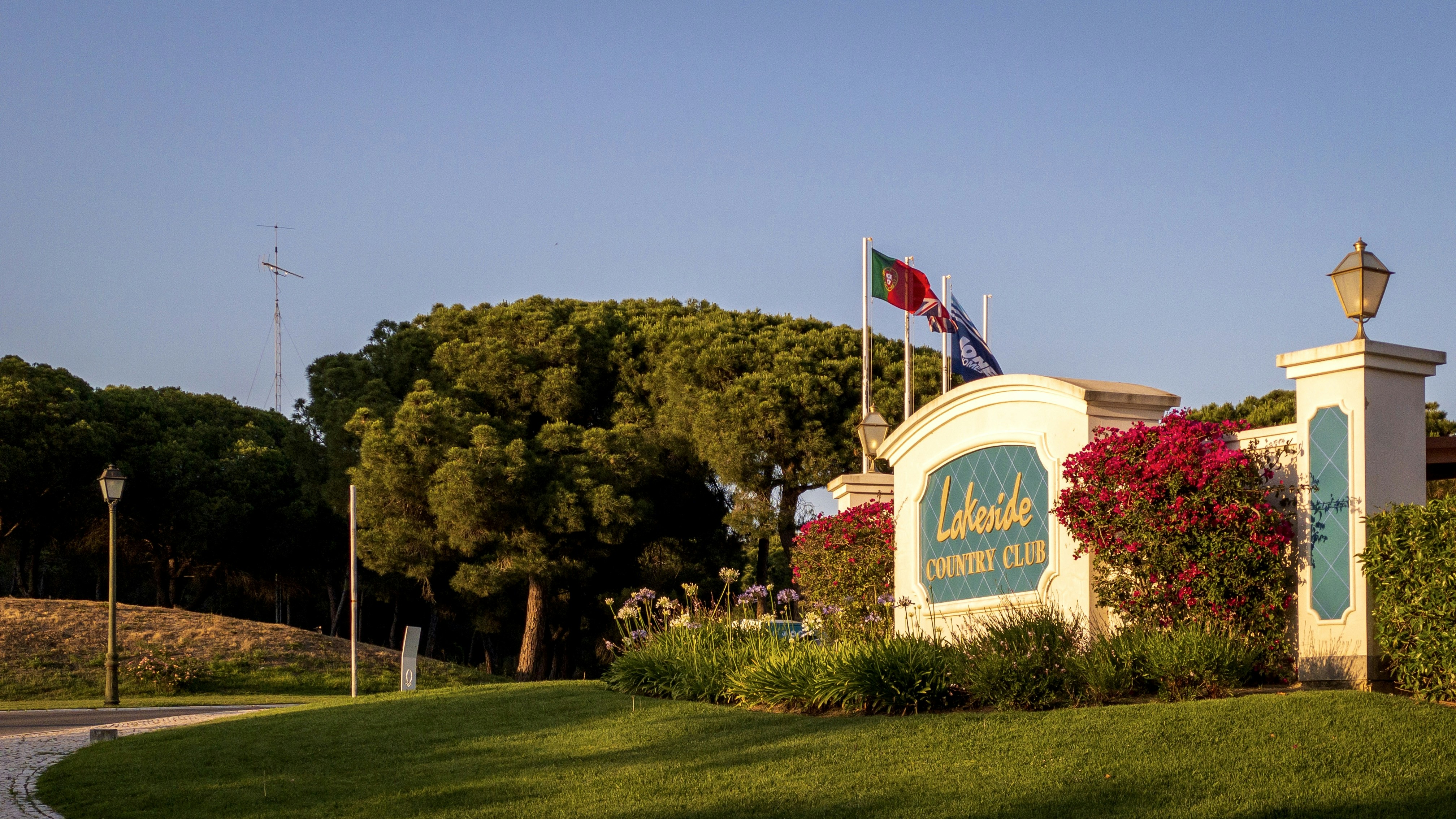 Resort sign surrounded by vibrant flowers and flags under a clear blue sky.
