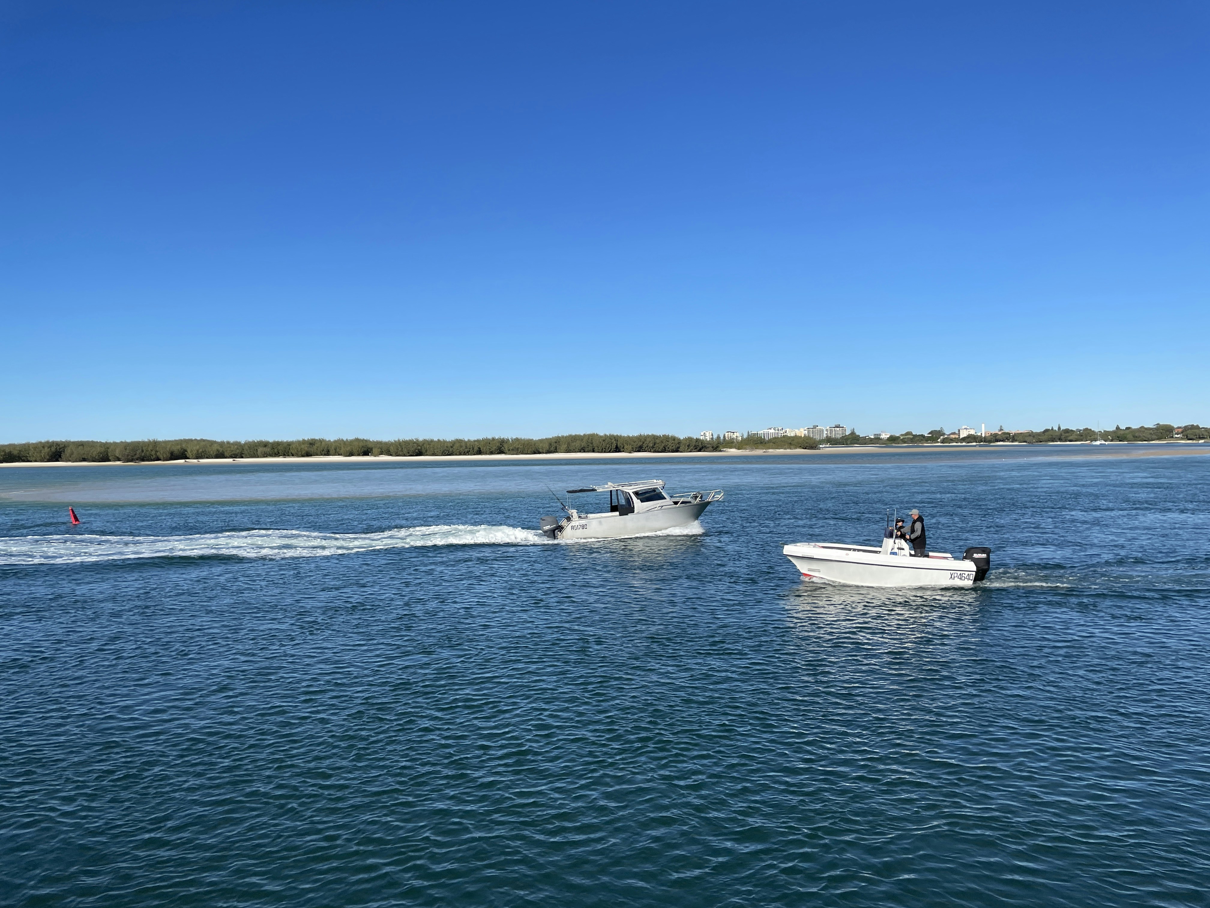 Two boats carving a wake across a sunlit coastal inlet