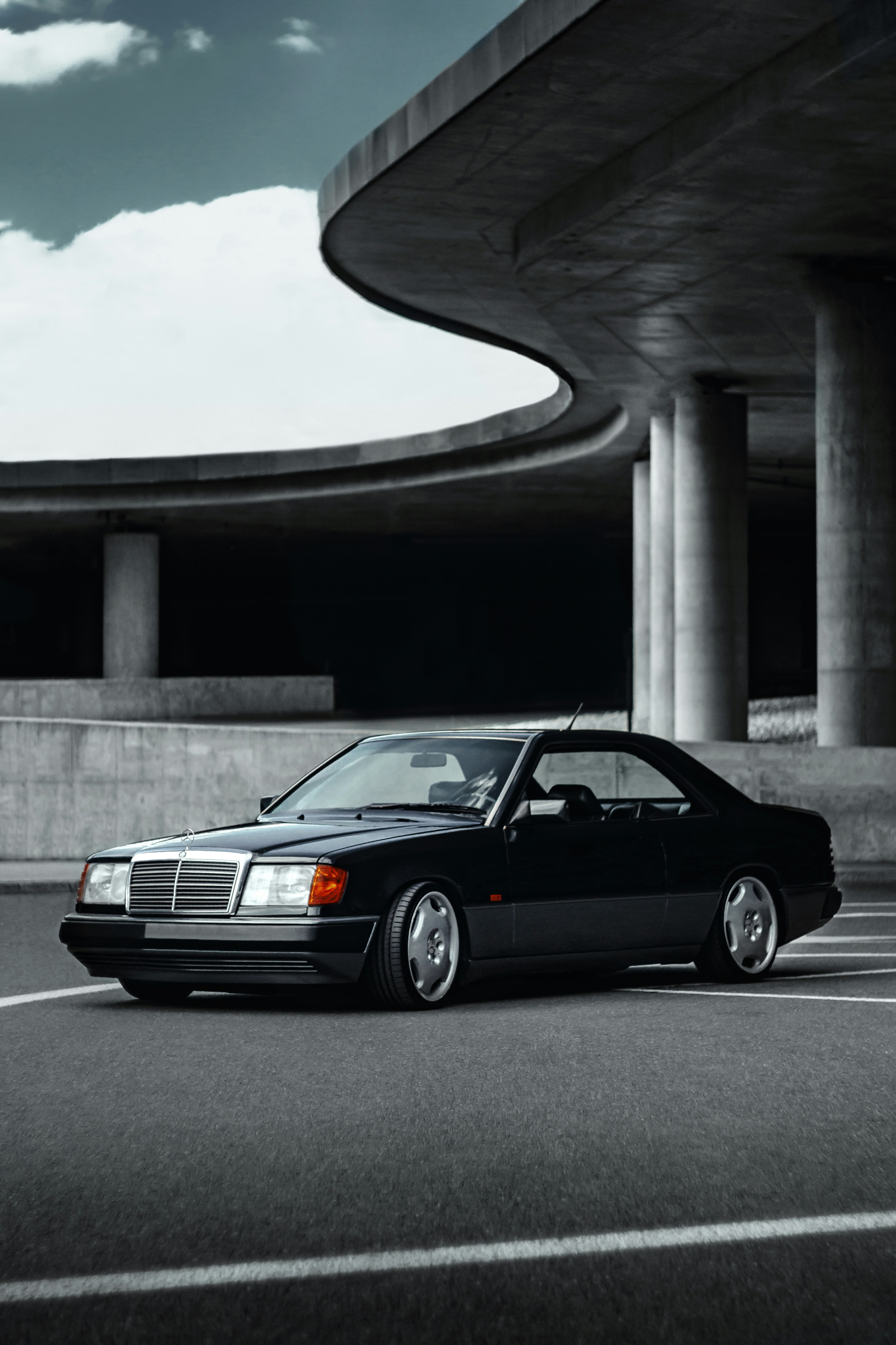 Sleek black coupe parked on a curved urban roadway beneath a concrete overpass, showcasing a blend of classic design and contemporary architecture.