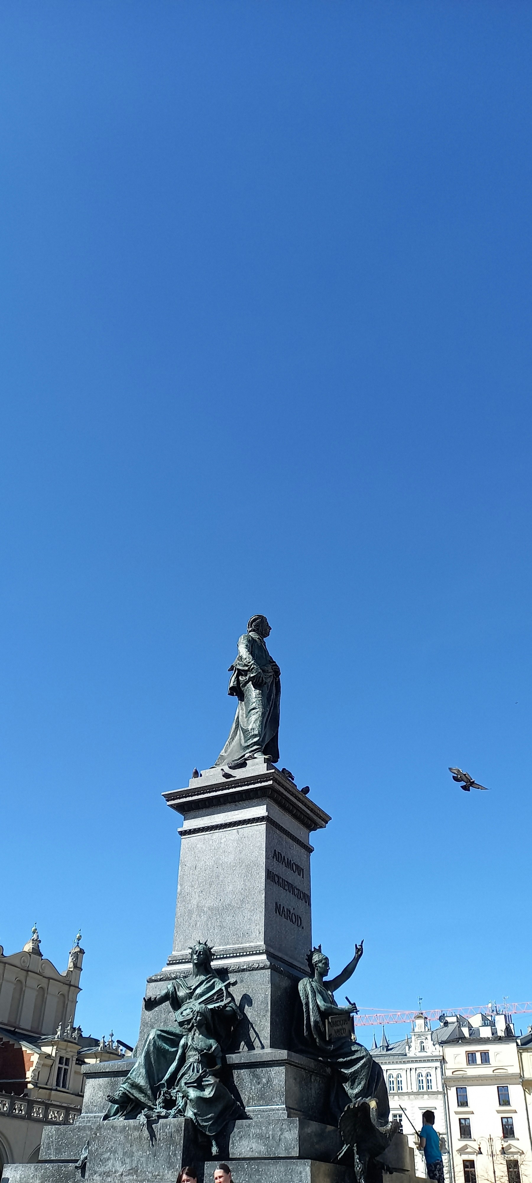 Bronze statue surrounded by intricate sculptures, set against a clear blue sky. The monument honors historical figures and their contributions.