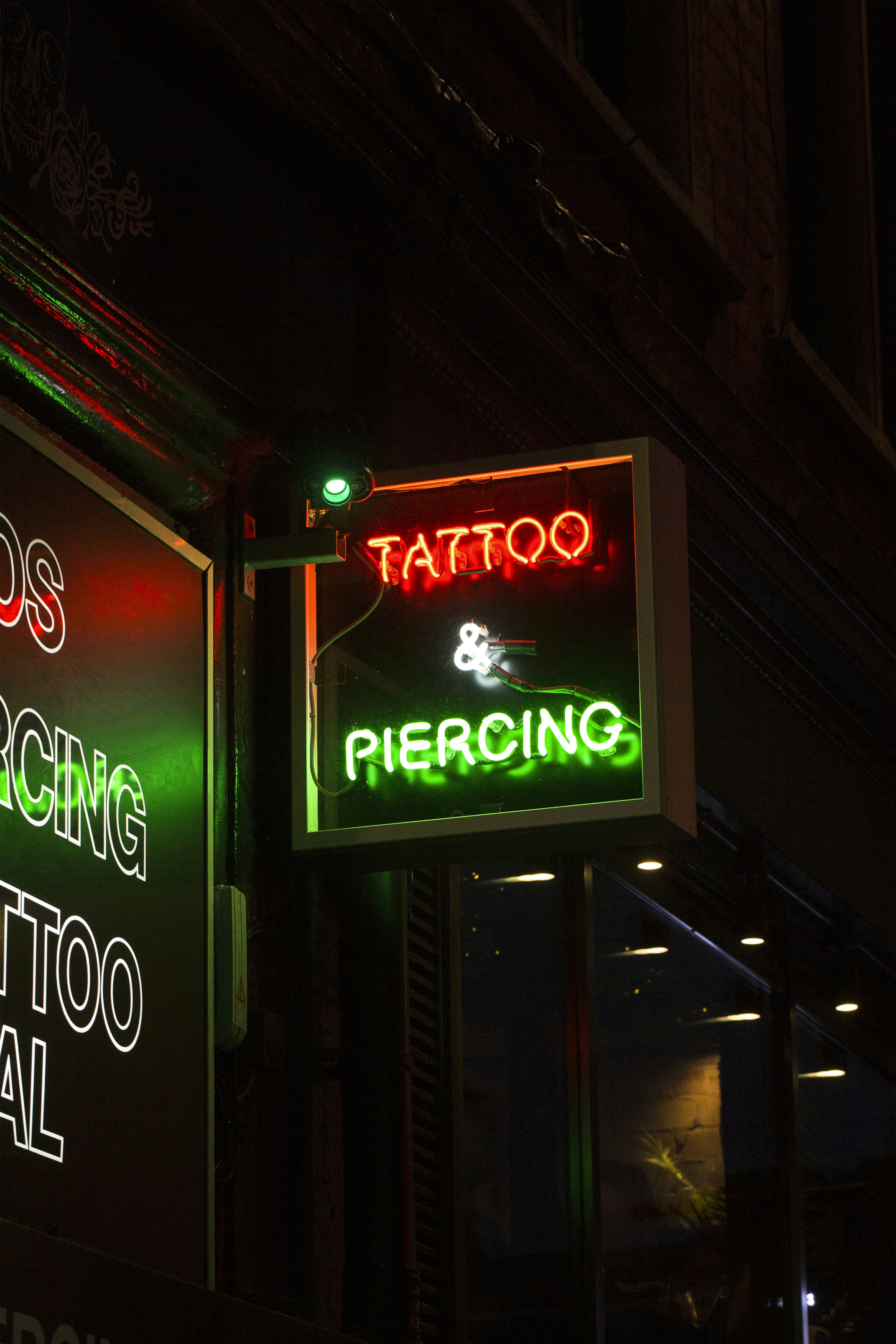 Neon sign displaying 'TATTOO & PIERCING' against a dark backdrop, highlighting the vibrant colors of the advertisement.