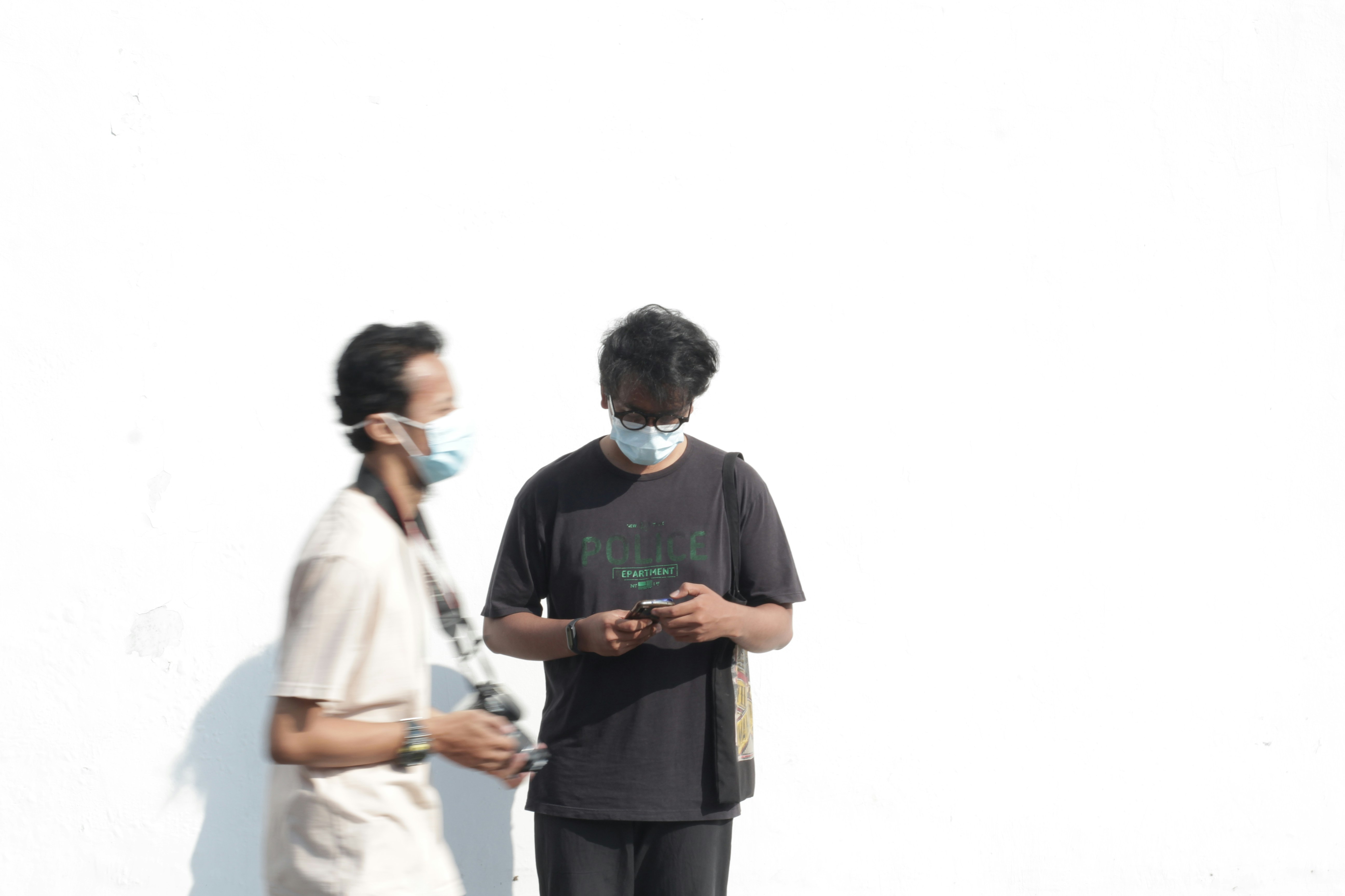 Two individuals wearing masks engage in conversation against a stark white background.