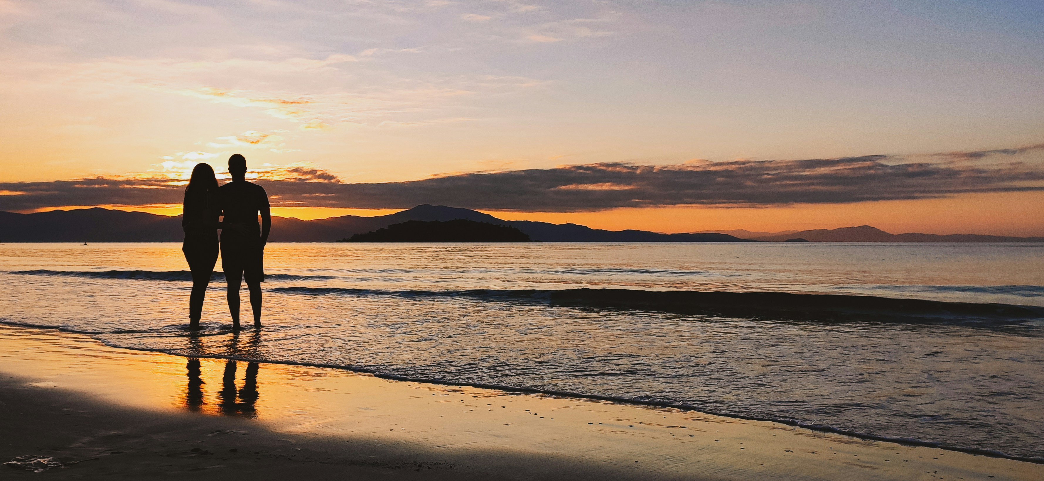 silhouette of mountain near body of water during sunset