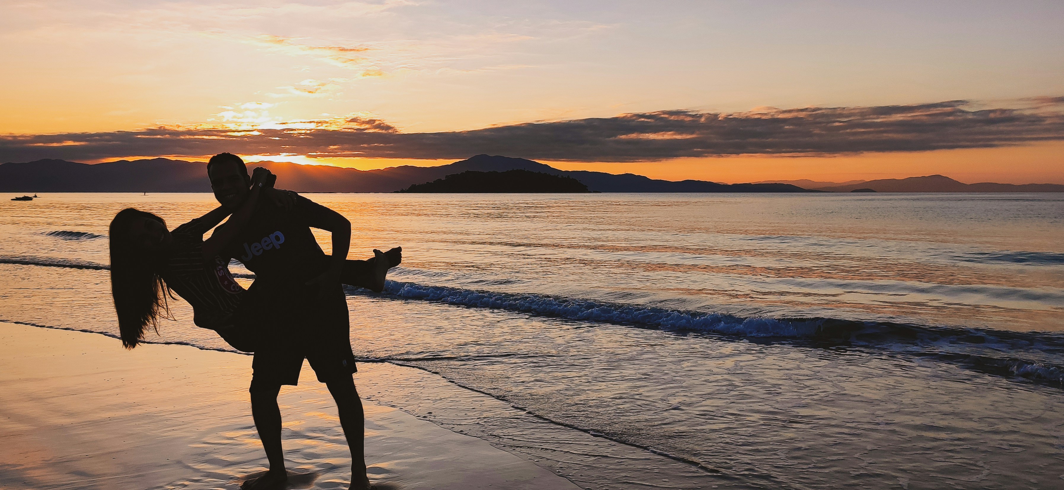 Silhouette of a couple dancing on the beach at sunset with vibrant sky and gentle waves.