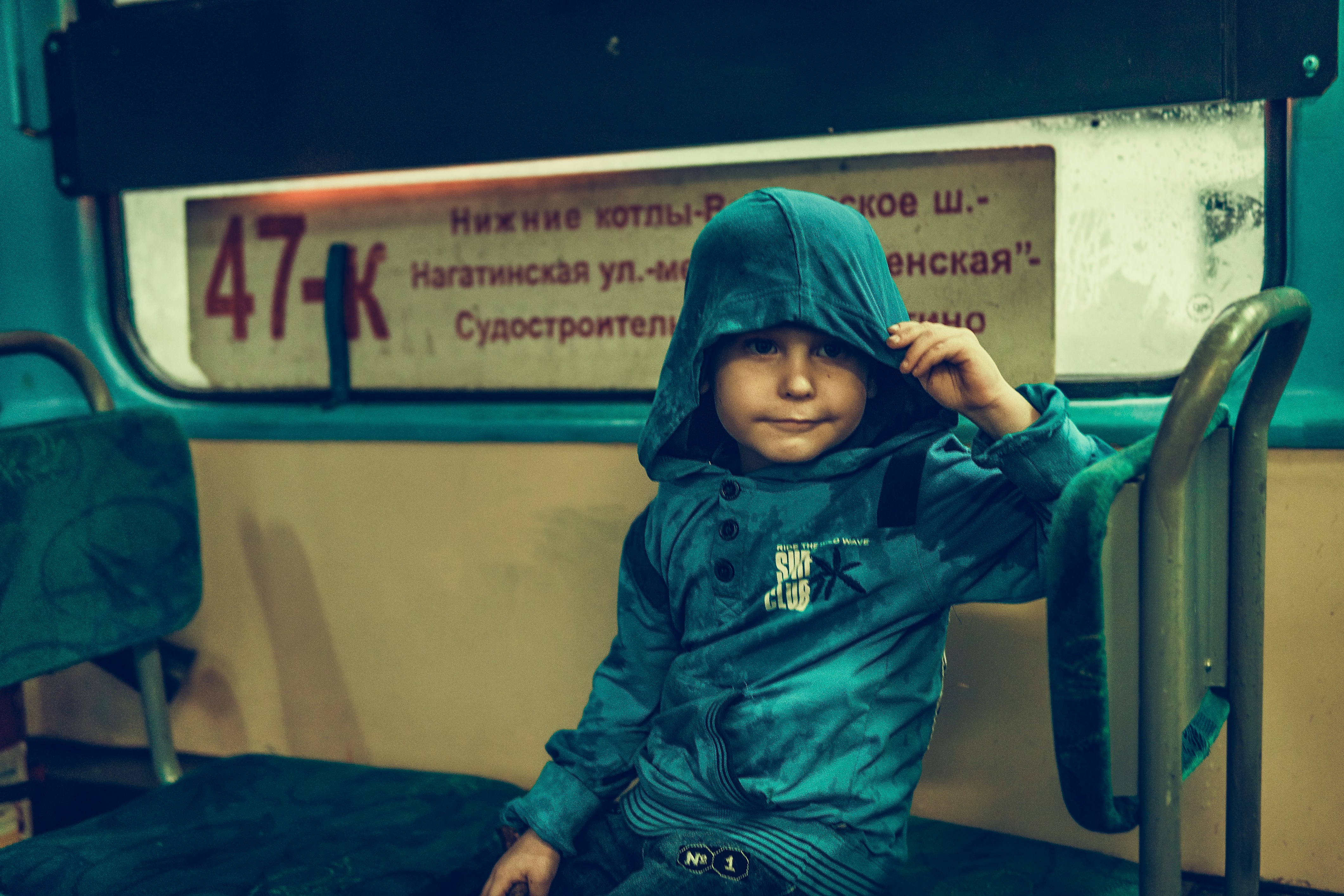 Young boy in a blue hoodie sitting on a bus seat, gazing thoughtfully while the cityscape passes by outside.
