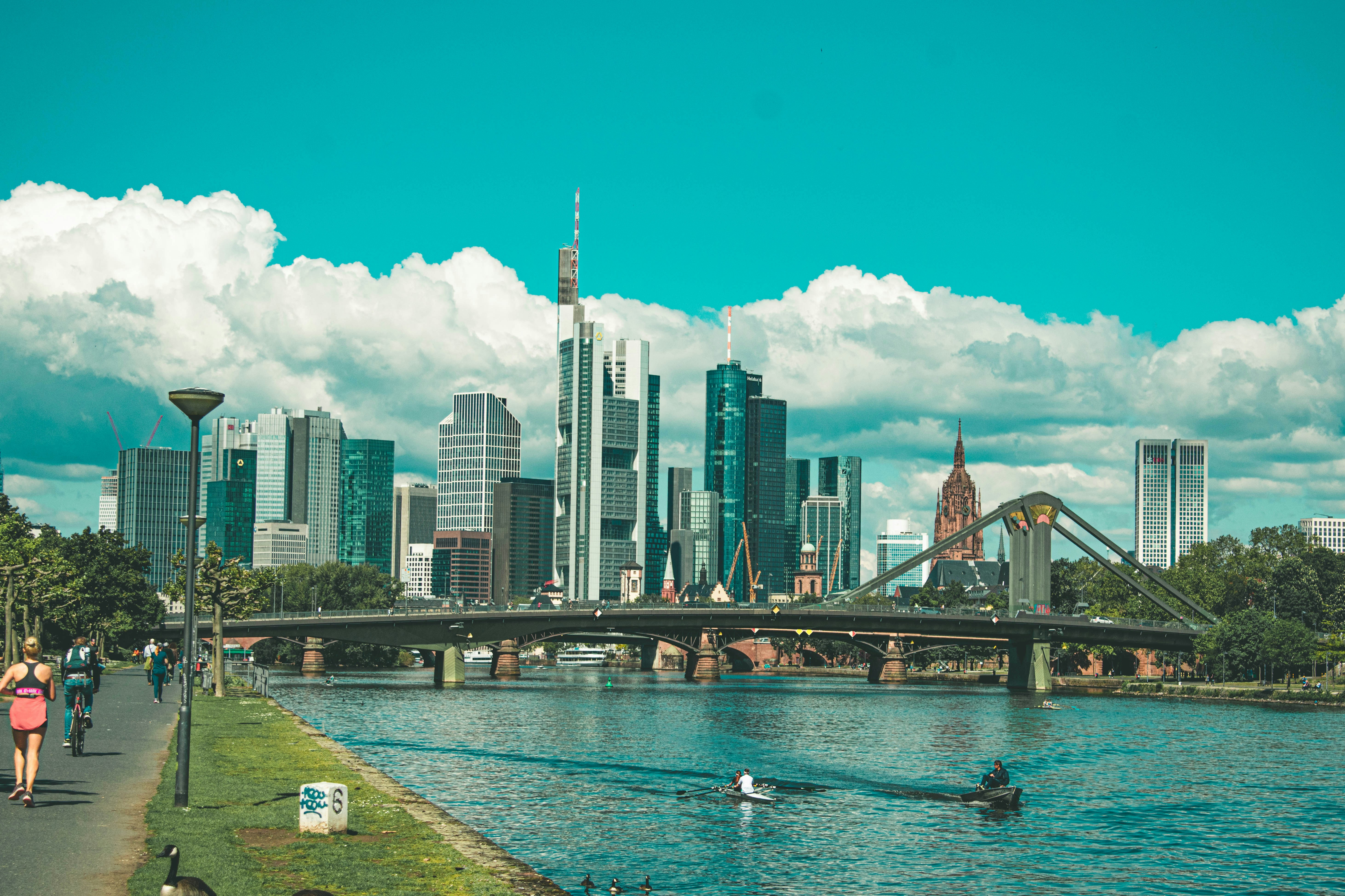 City skyline with modern skyscrapers and a historic church, framed by lush greenery and a serene river. The scene captures the dynamic interplay between urban life and nature.