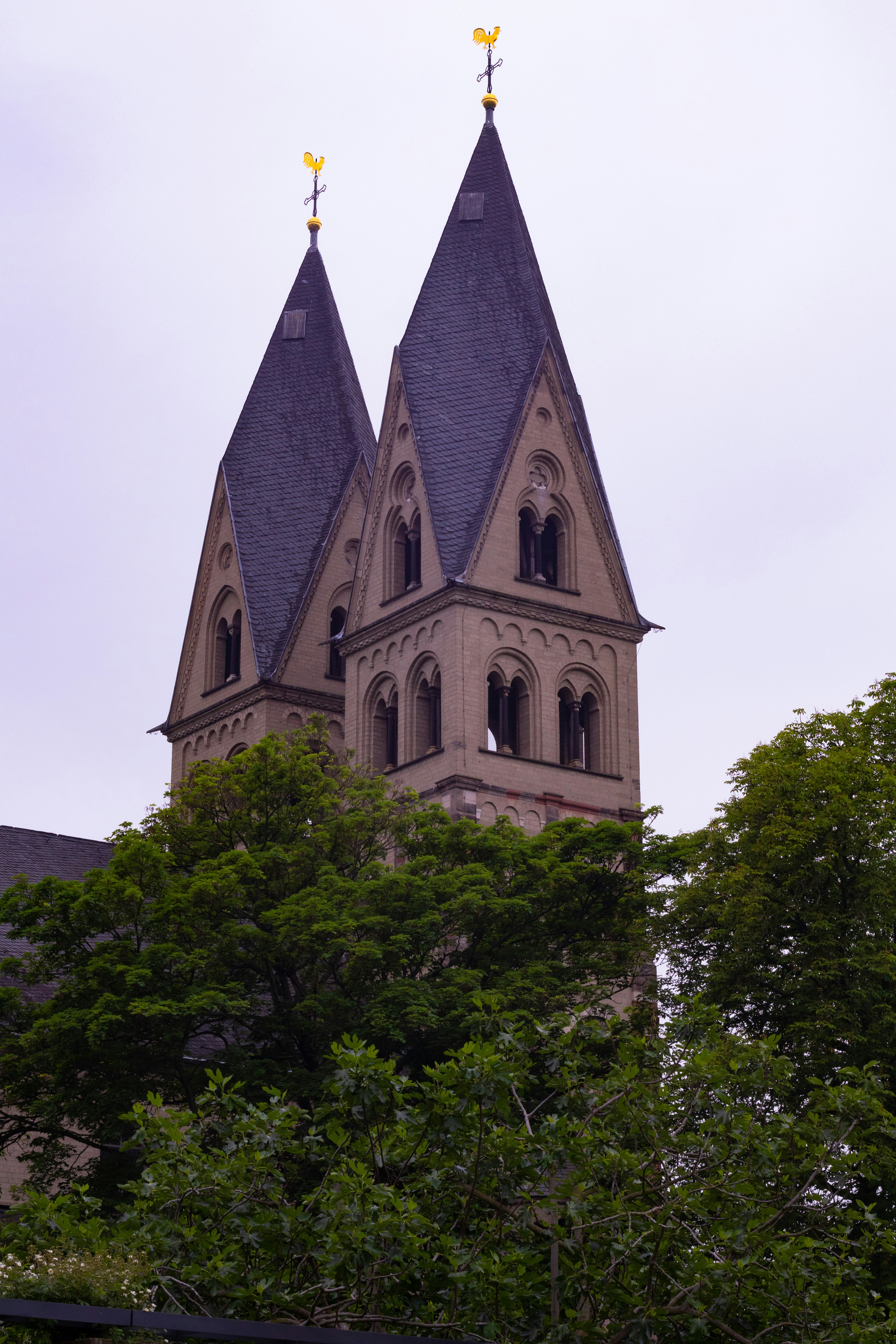 Gothic-style church spires rise above lush green trees under an overcast sky.