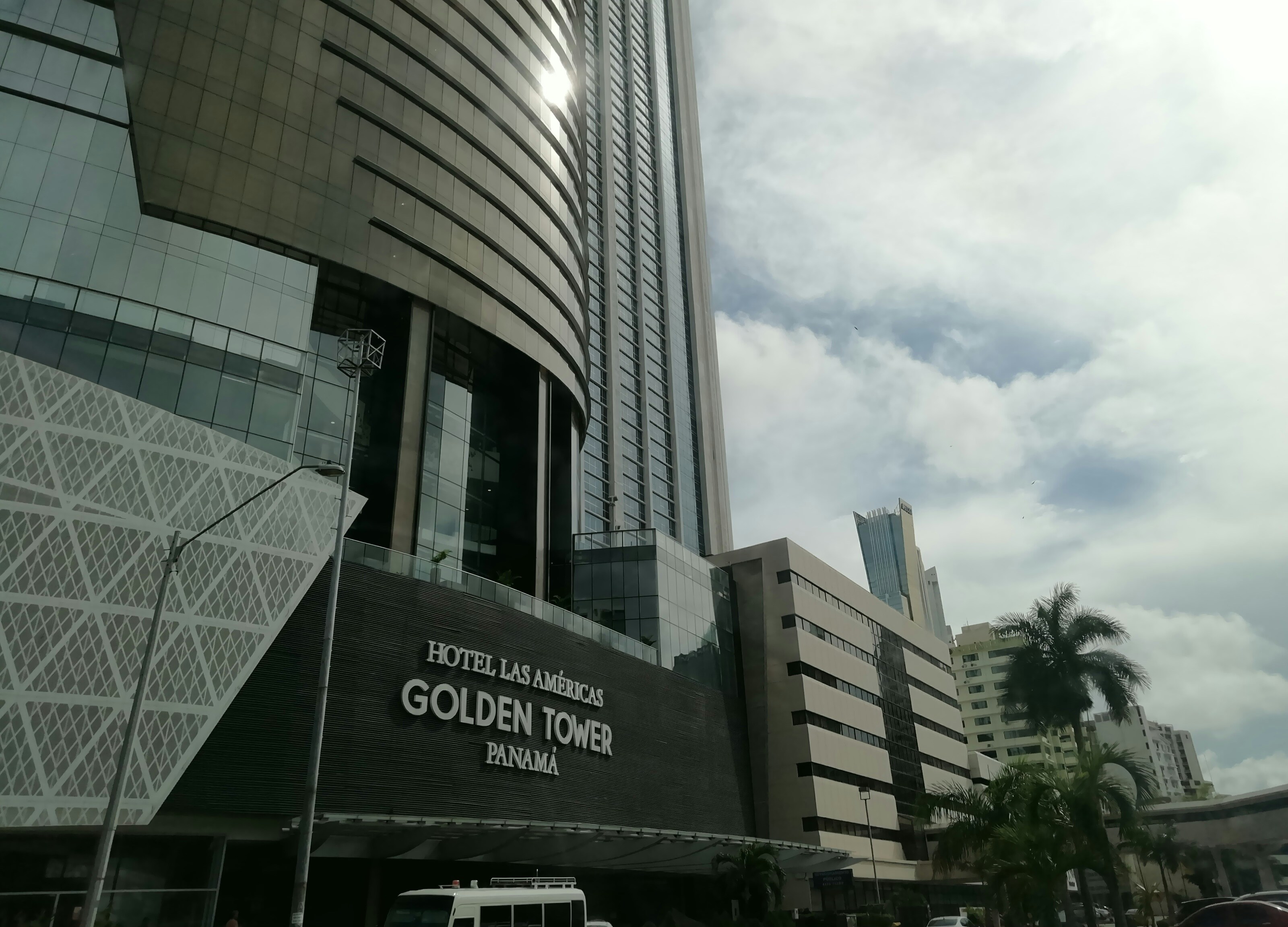 Modern skyscrapers rise against a partially cloudy sky, with palm trees adding a touch of greenery to the urban scene.