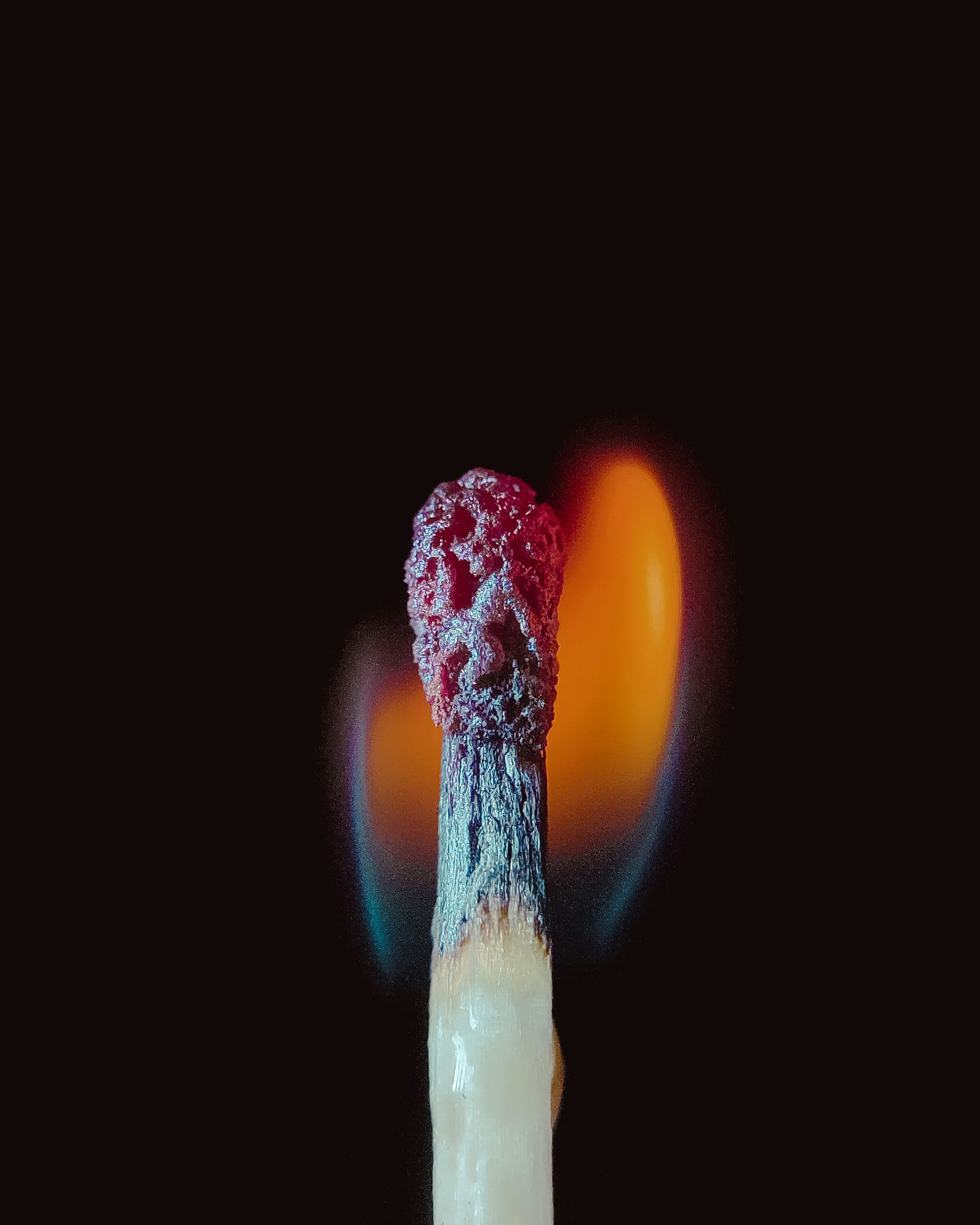 Macro shot of a singed match head with a glowing ember against a deep black background.