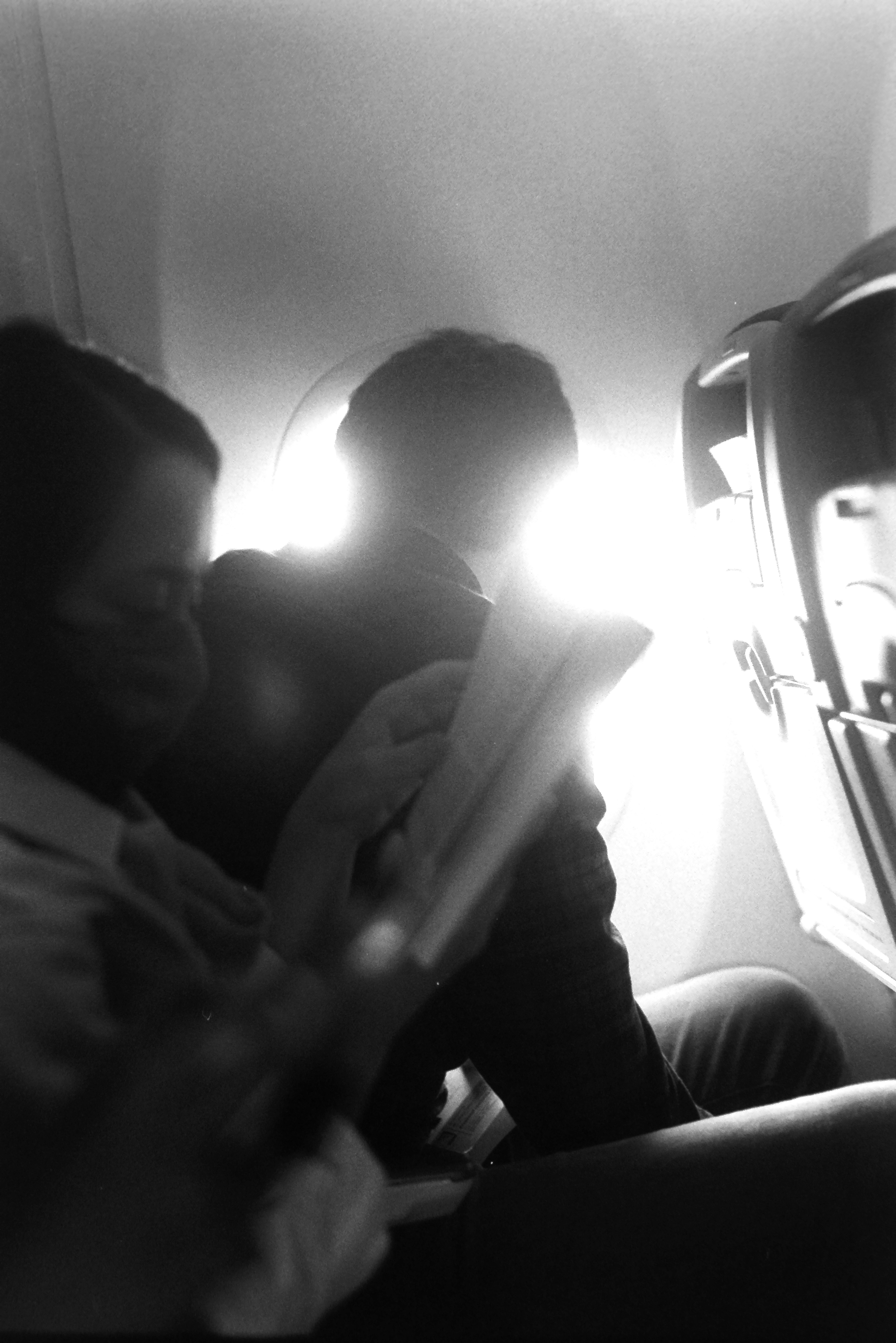 Passengers engrossed in reading during a flight, with sunlight illuminating the scene from the window.
