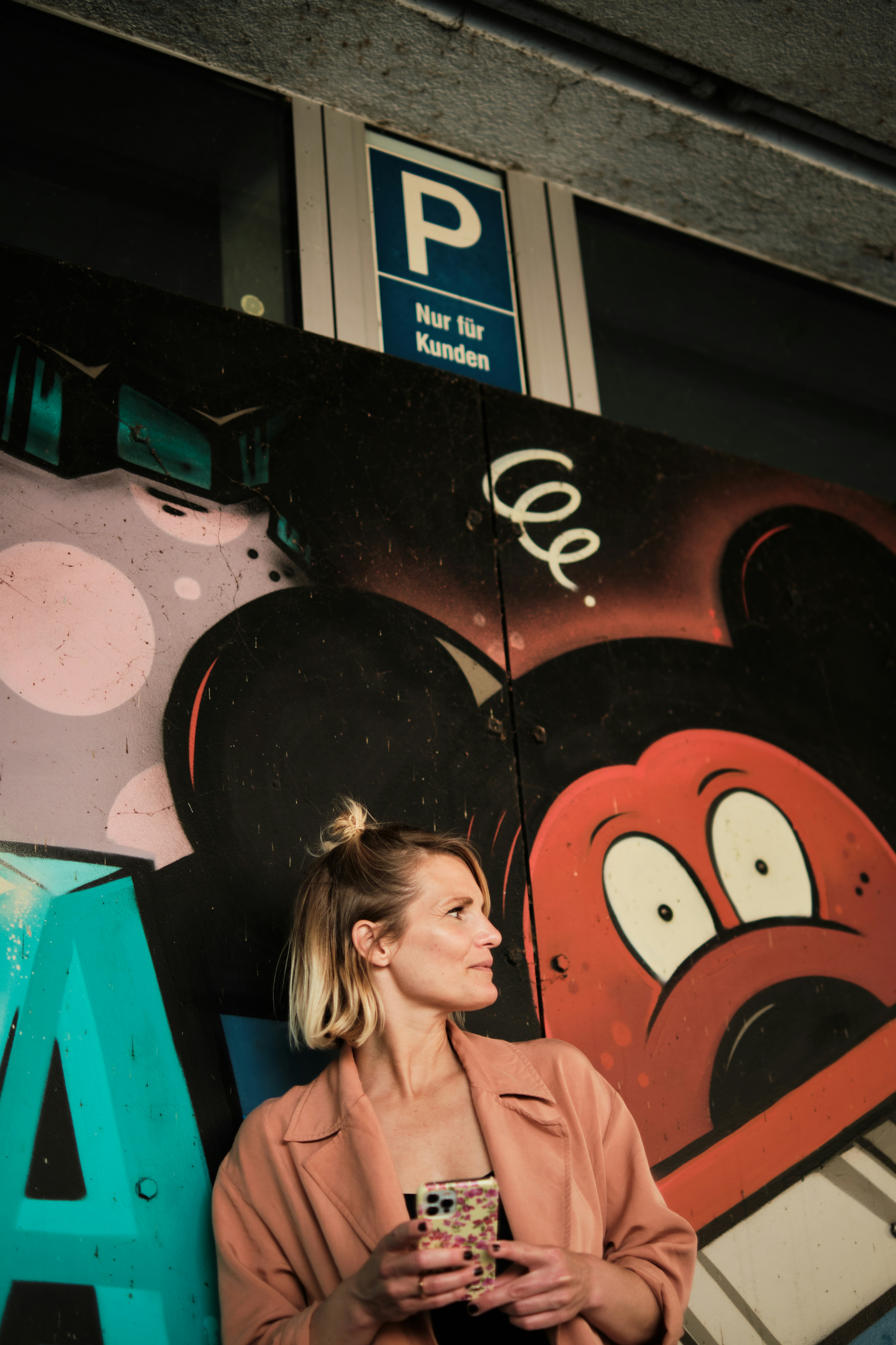 Pastel Coat, Neon Wall: A Quiet Portrait by a Cartoon Graffiti Mural