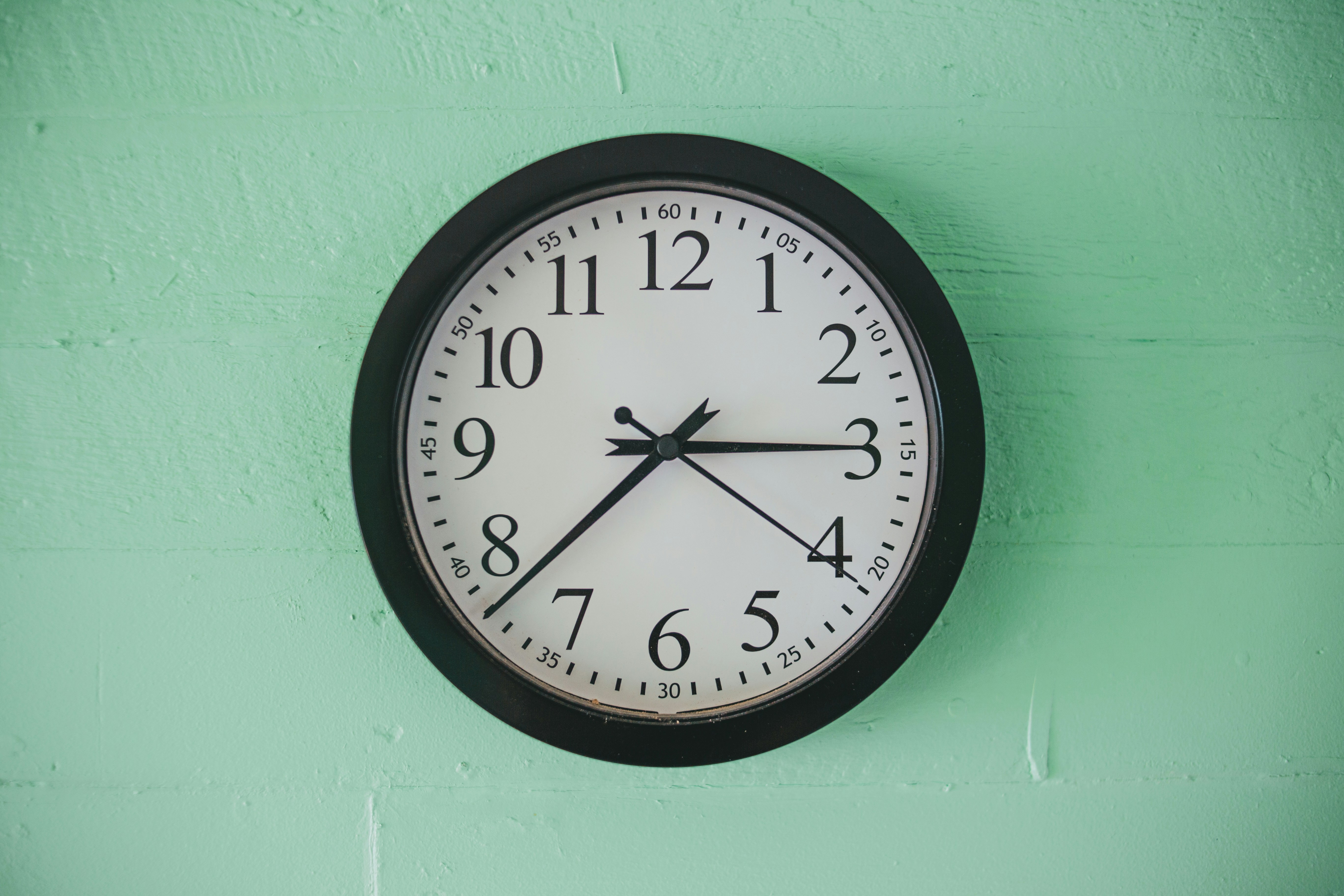 Wall clock with black frame and white face displaying the time against a mint green background.