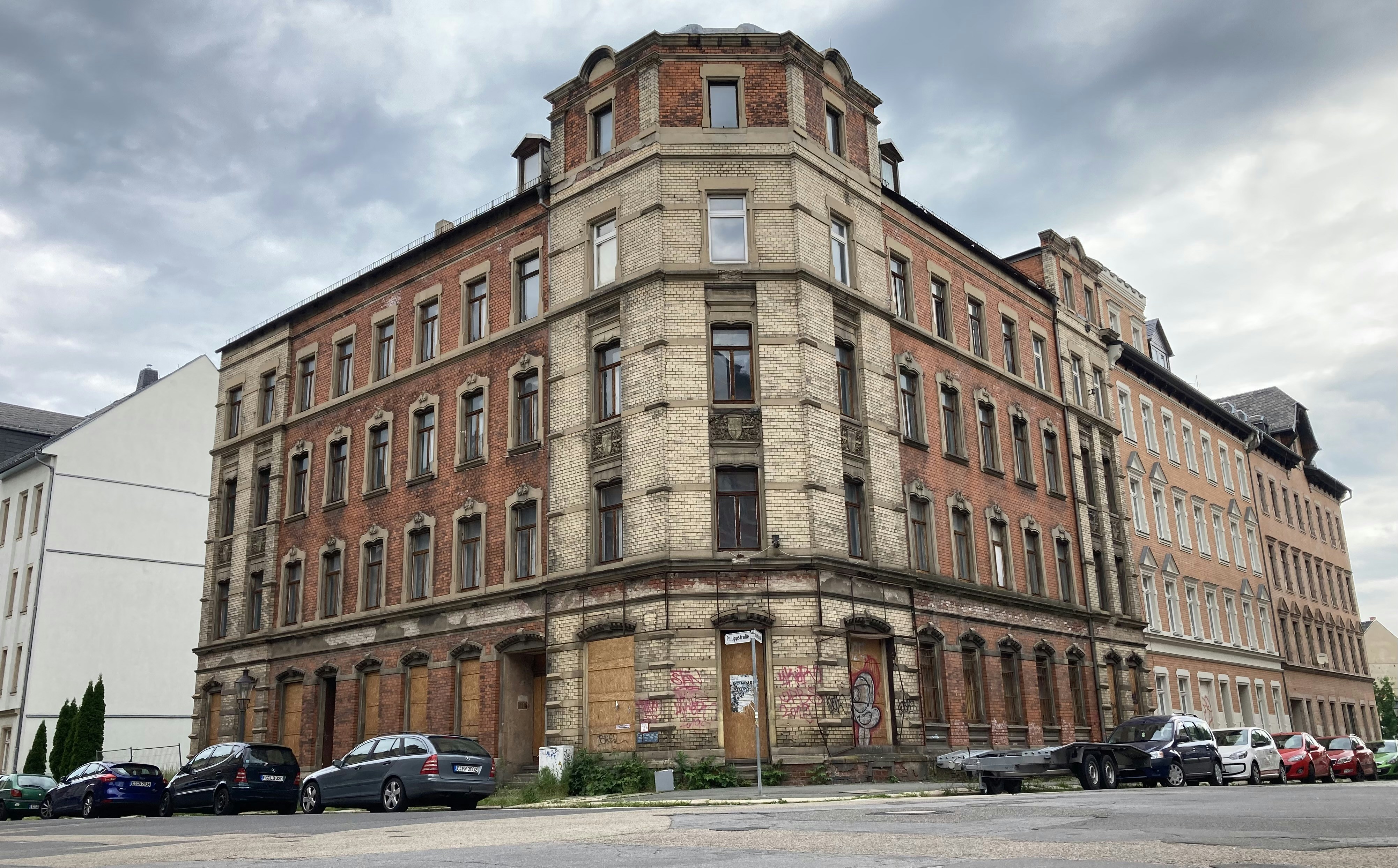 Aged brick corner building with boarded windows under a cloudy sky.