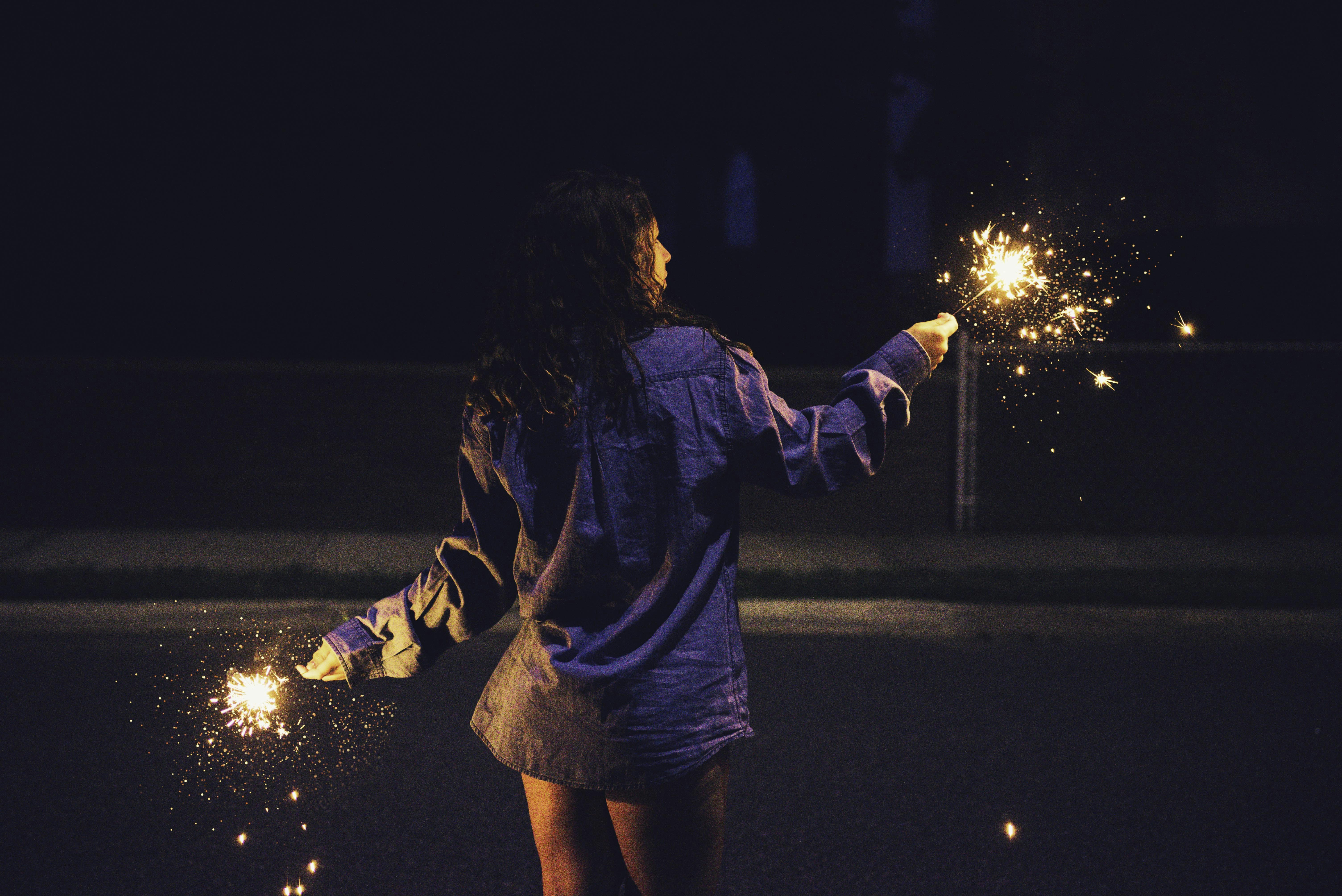 A person holding sparklers in each hand, creating a magical display of light against a dark backdrop.