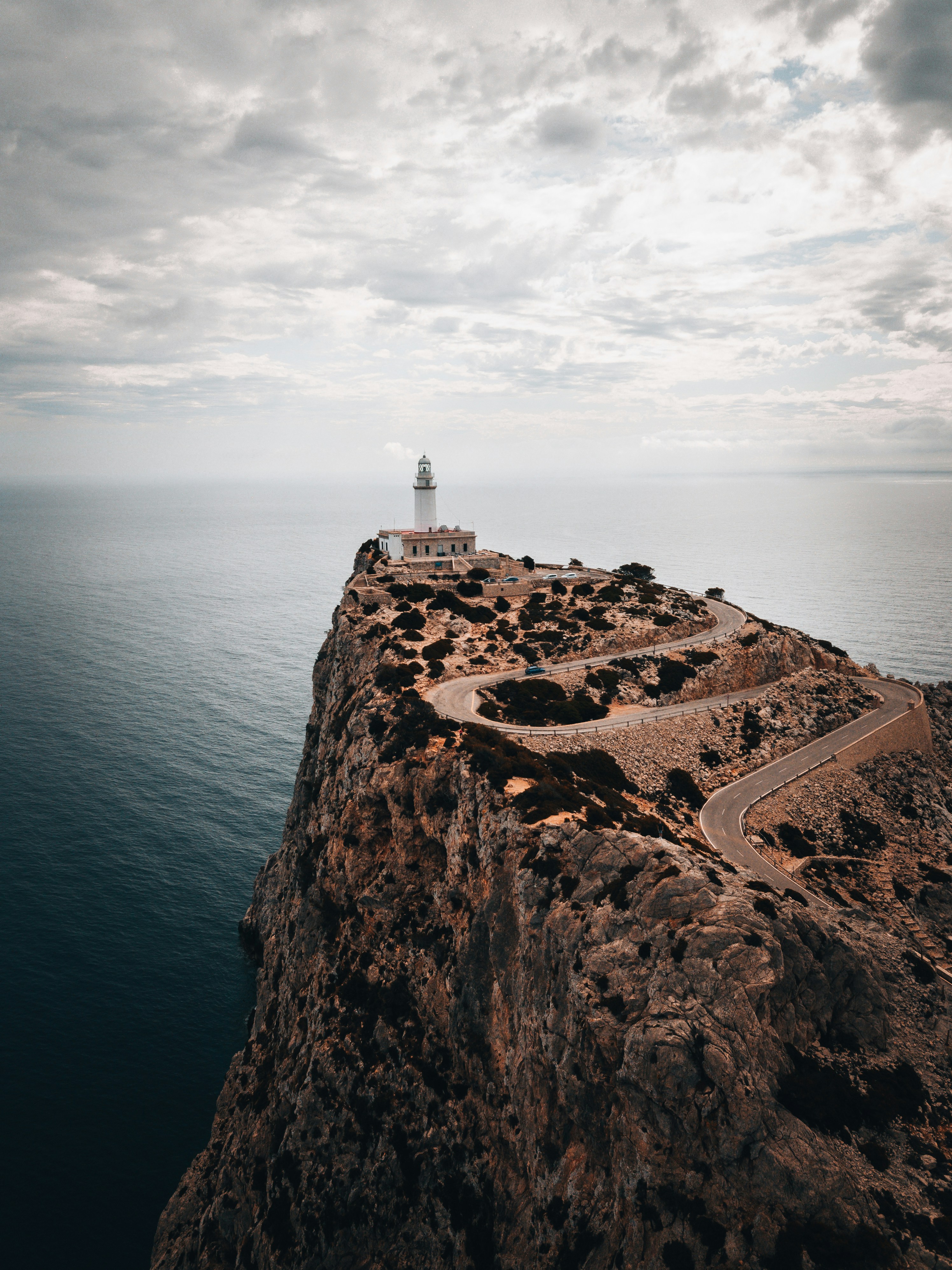 White and brown lighthouse on brown rock formation near body of water ...