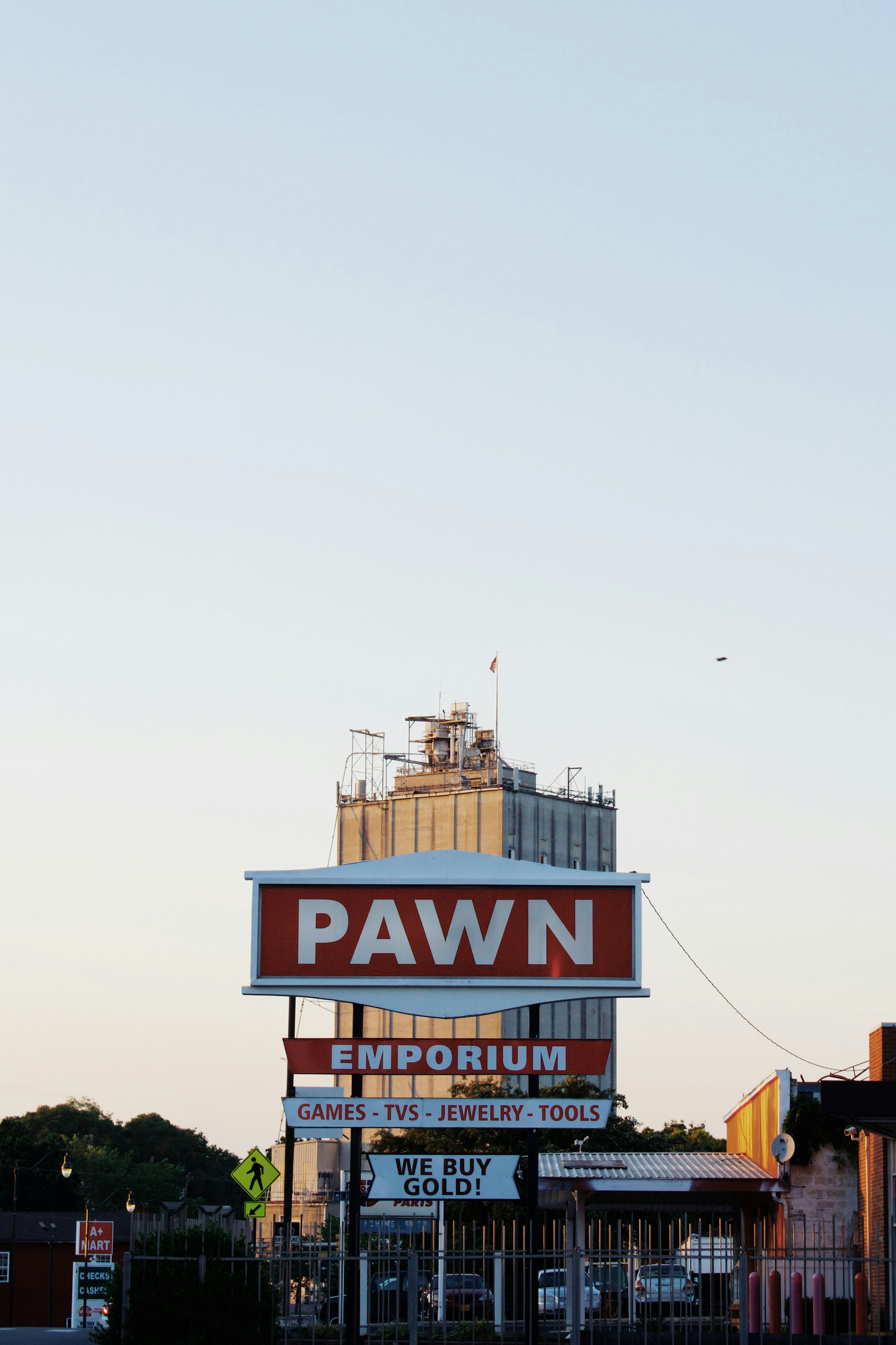 A pawn shop sign prominently displayed against a clear sky, highlighting various items for sale including games, TVs, and jewelry.
