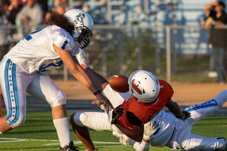 High-school football players collide as a loose football floats between helmets and outstretched hands.