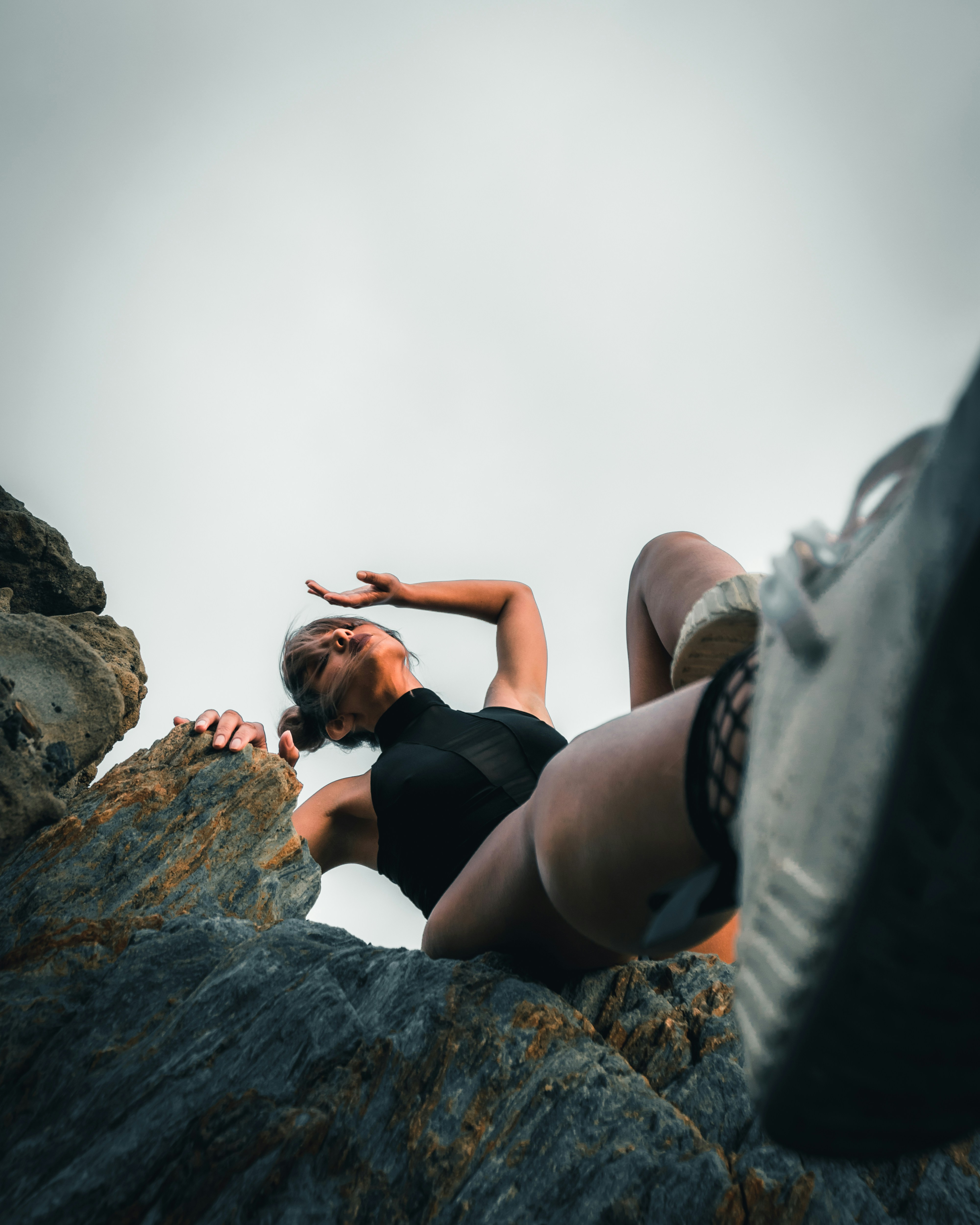 A climber in a black outfit gracefully navigates rocky terrain, showcasing strength and agility against a cloudy sky.