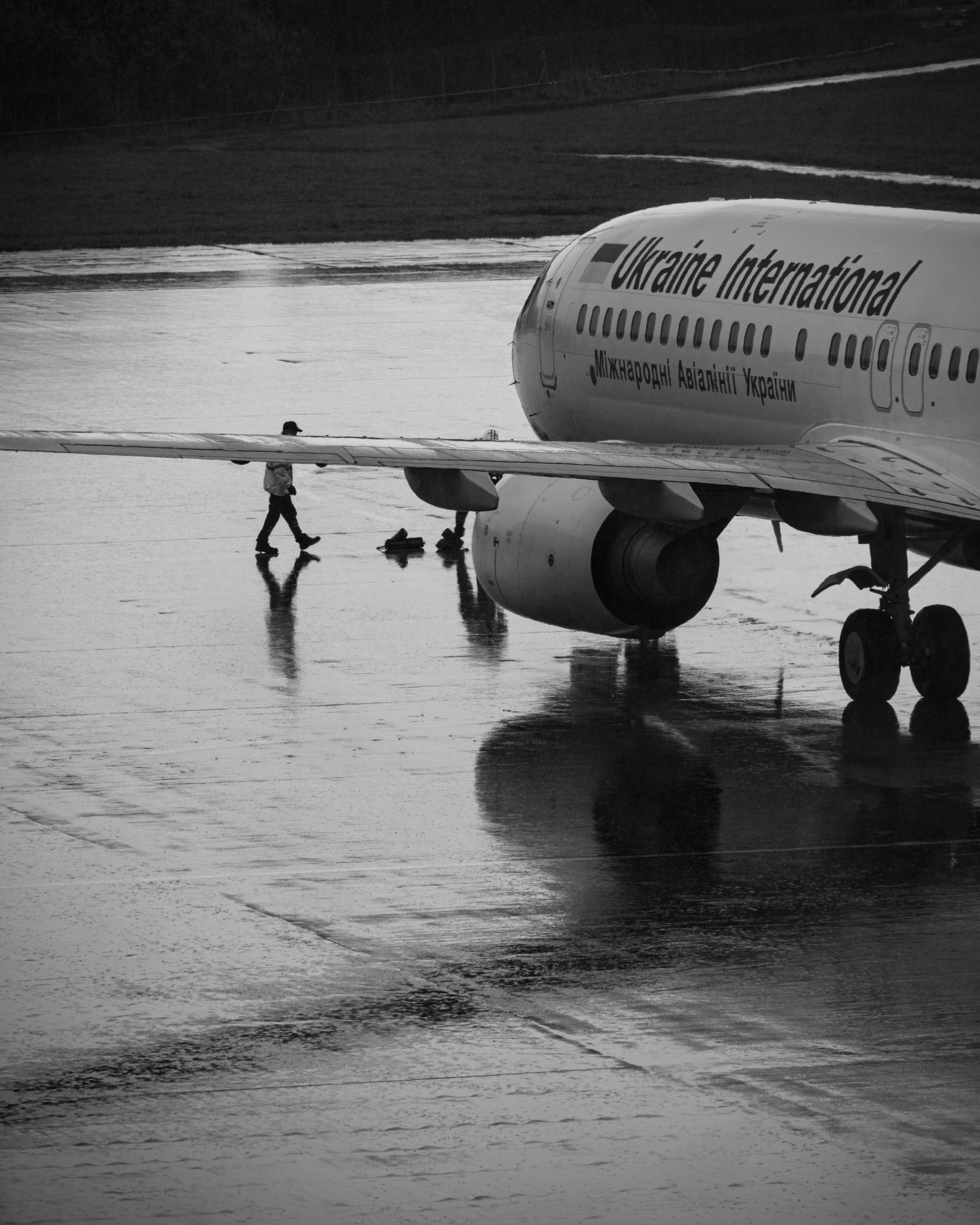 Glimmering Runway: A lone ground crewman beside a grounded Ukraine International jet