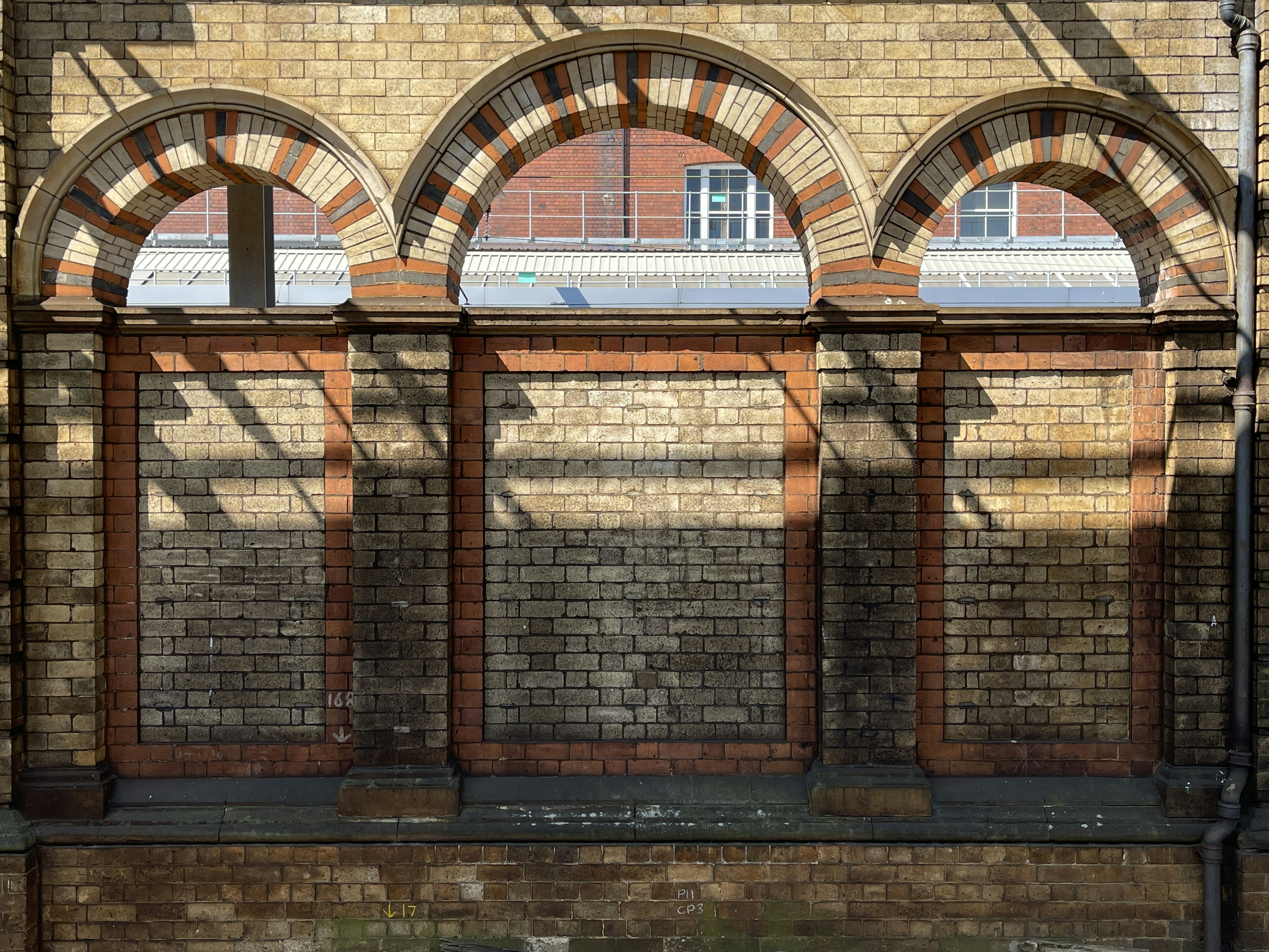 Brick building facade with arched windows casting geometric shadows onto the wall.